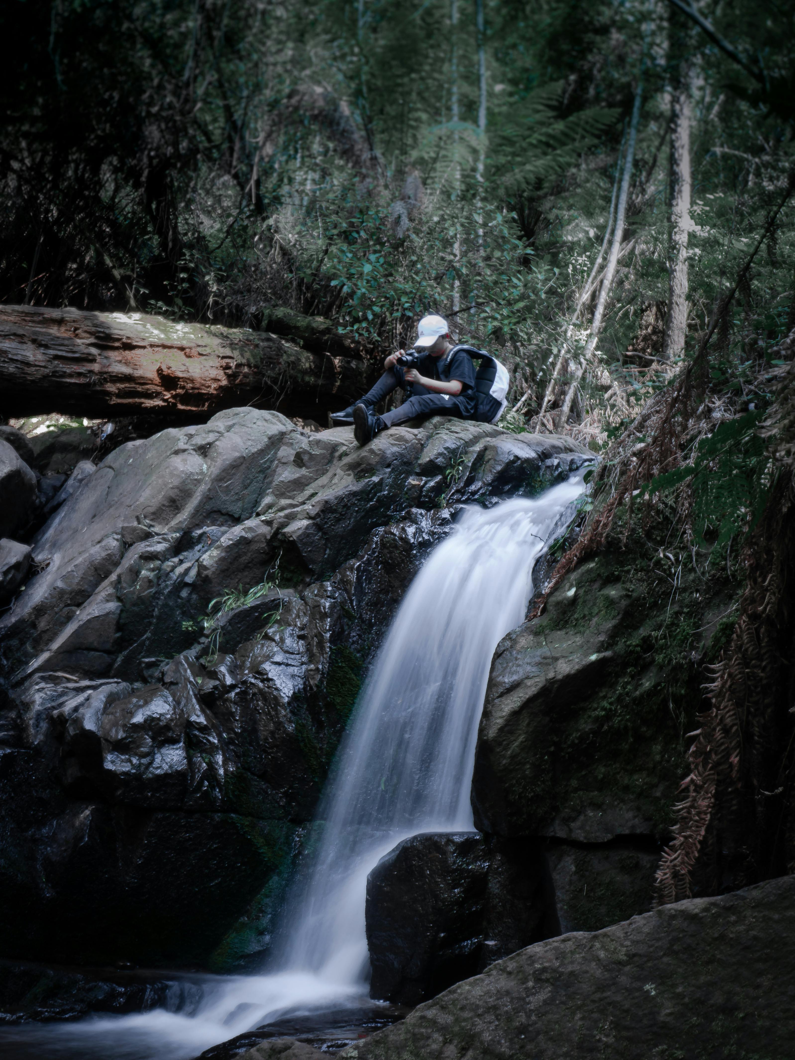 A Photographer Sitting on Rocks Beside a Waterfall · Free Stock Photo