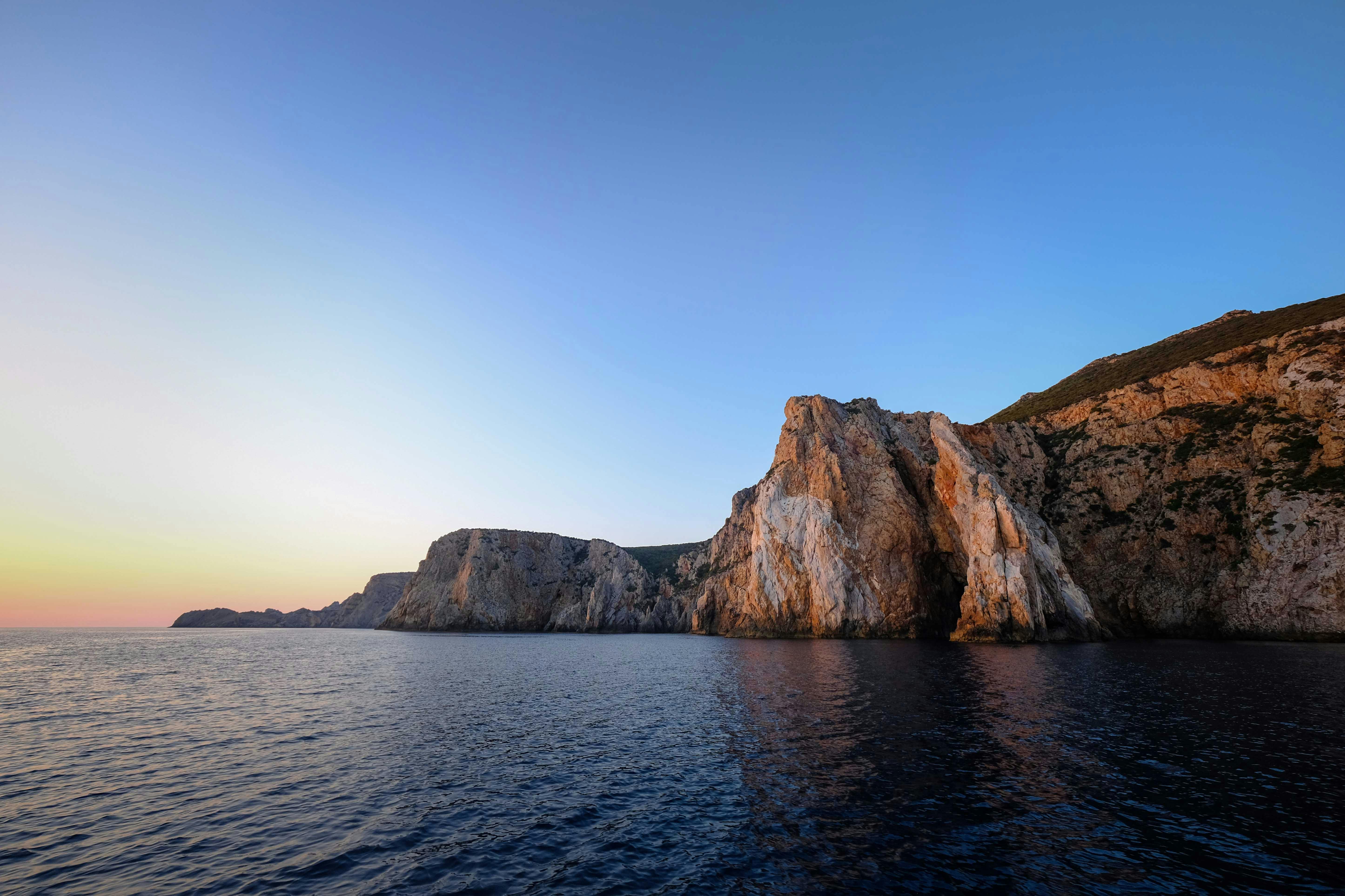 Mountain with cliffs in ocean at sundown · Free Stock Photo