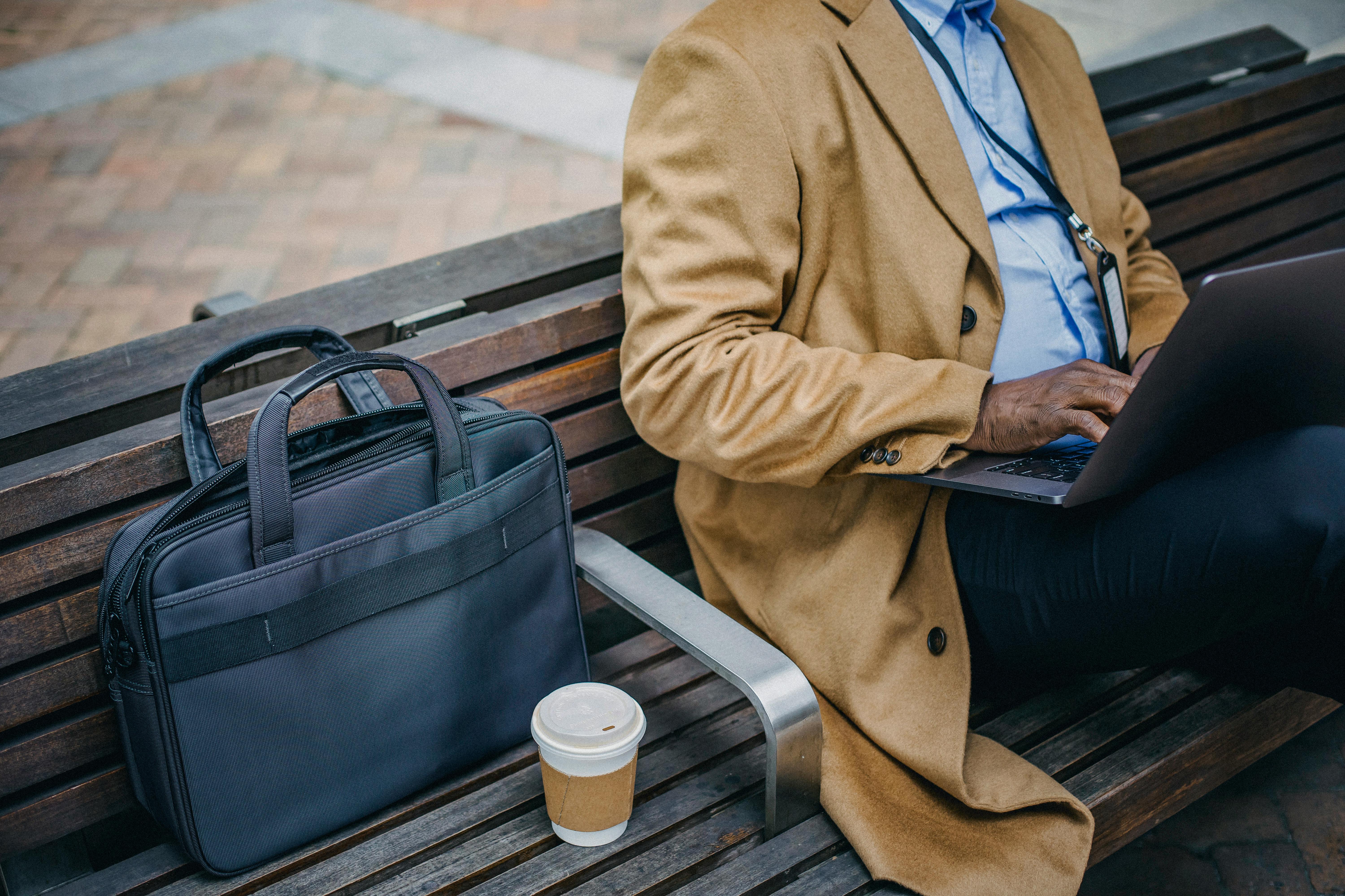 Crop faceless black man using laptop on street bench · Free Stock Photo