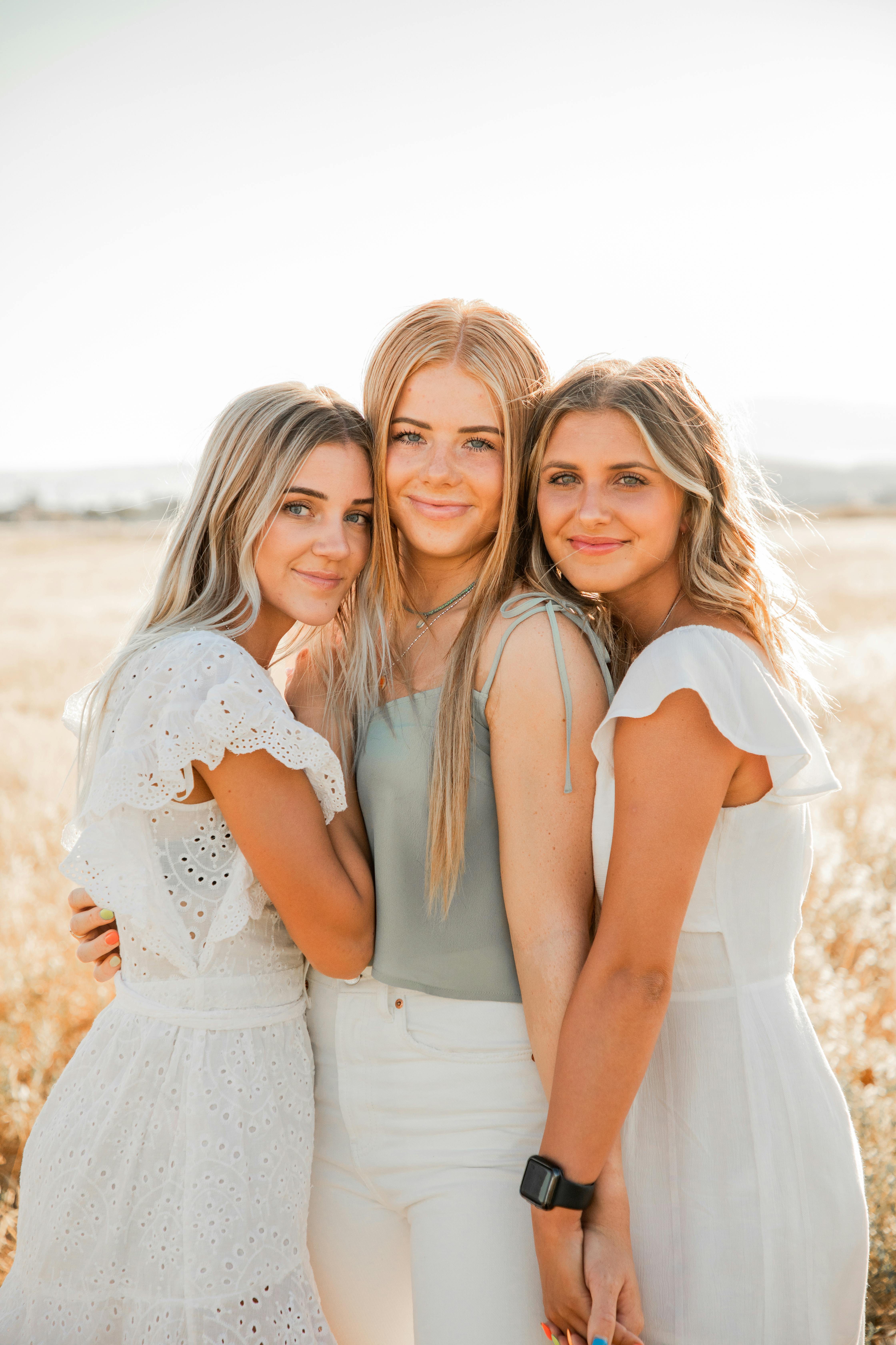 Stylish glad girlfriends embracing in countryside field in sunlight ...