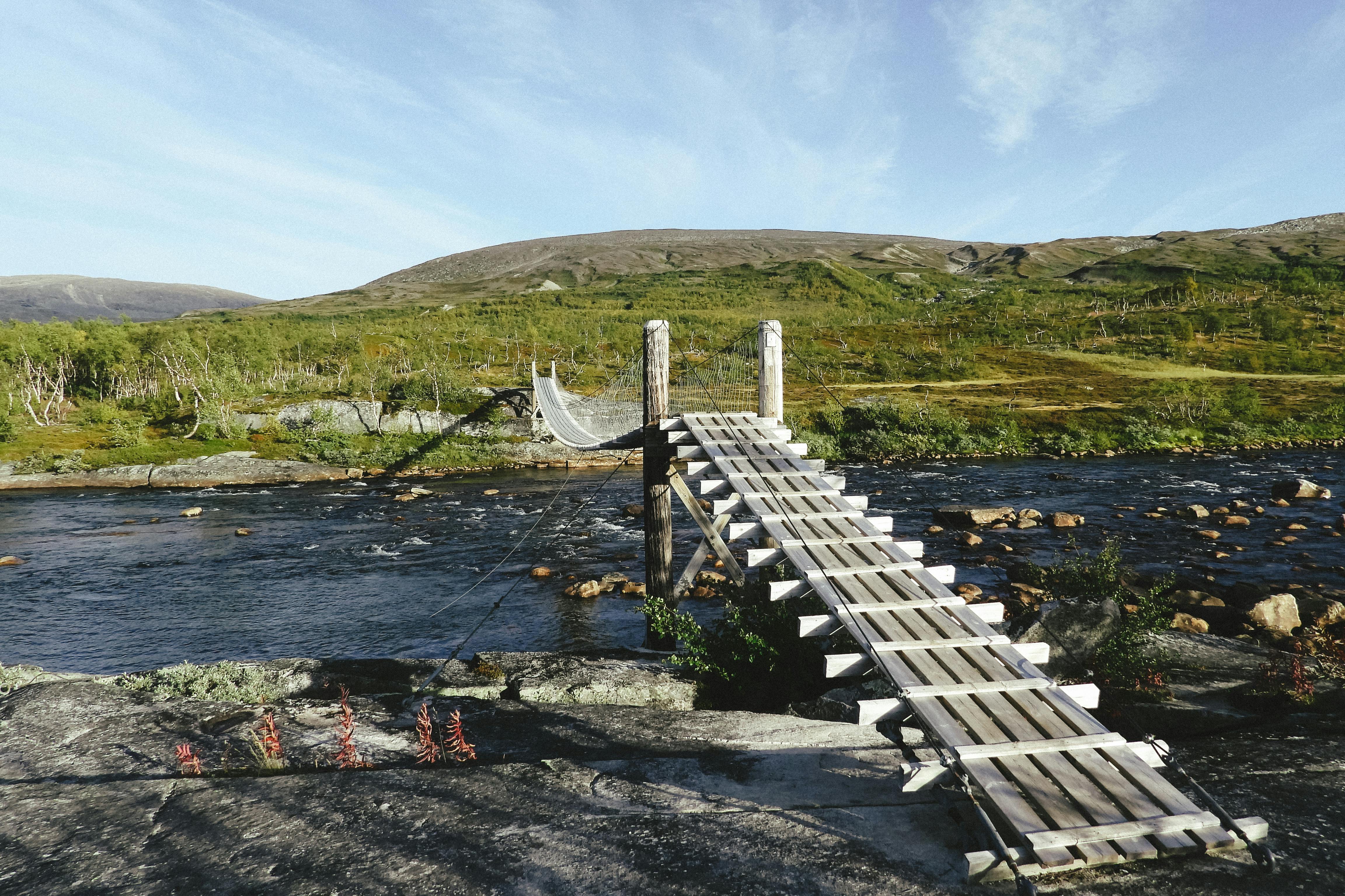 Wooden footbridge over river in hilly valley · Free Stock Photo