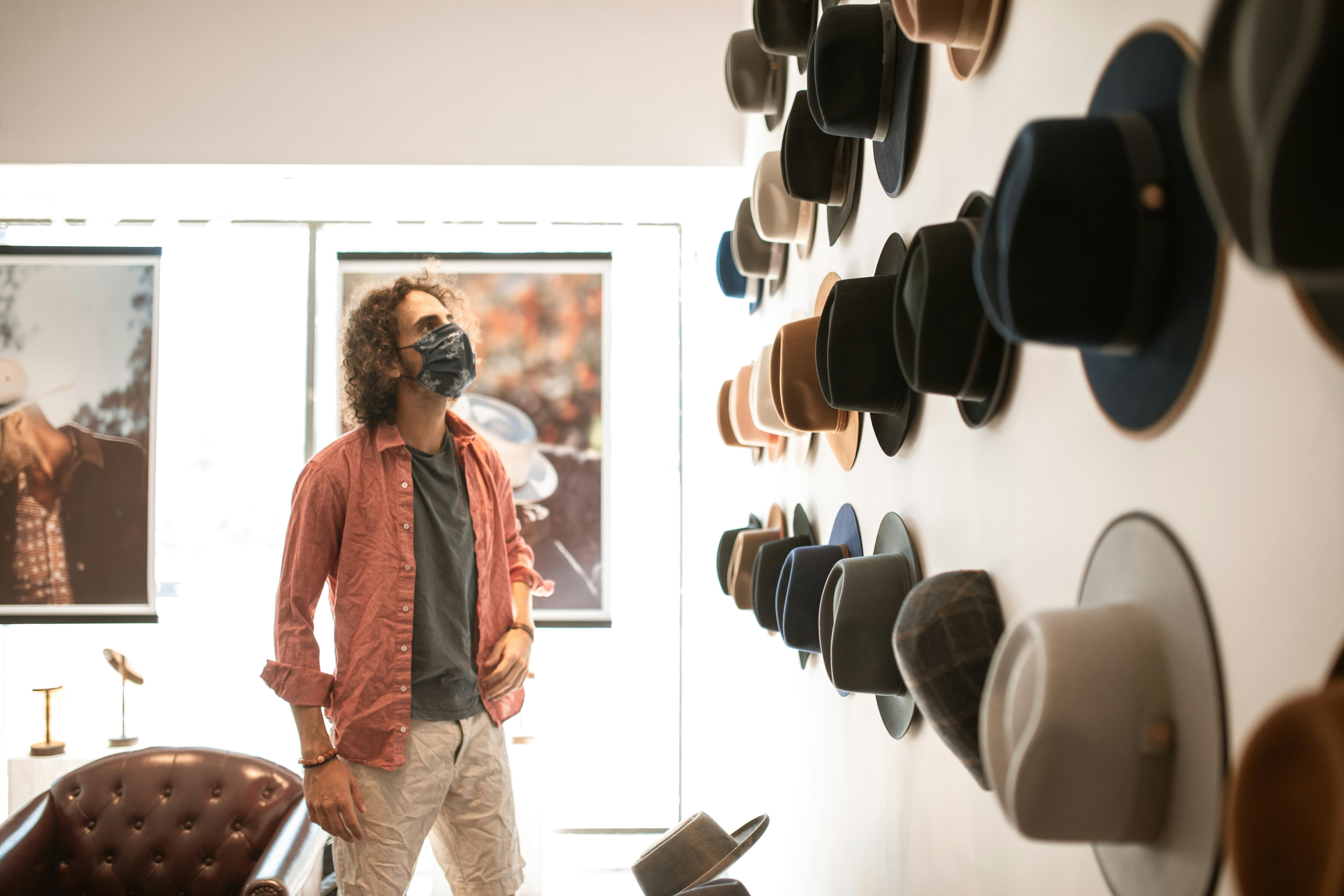 Man Looking at Wall and Choosing Hats · Free Stock Photo