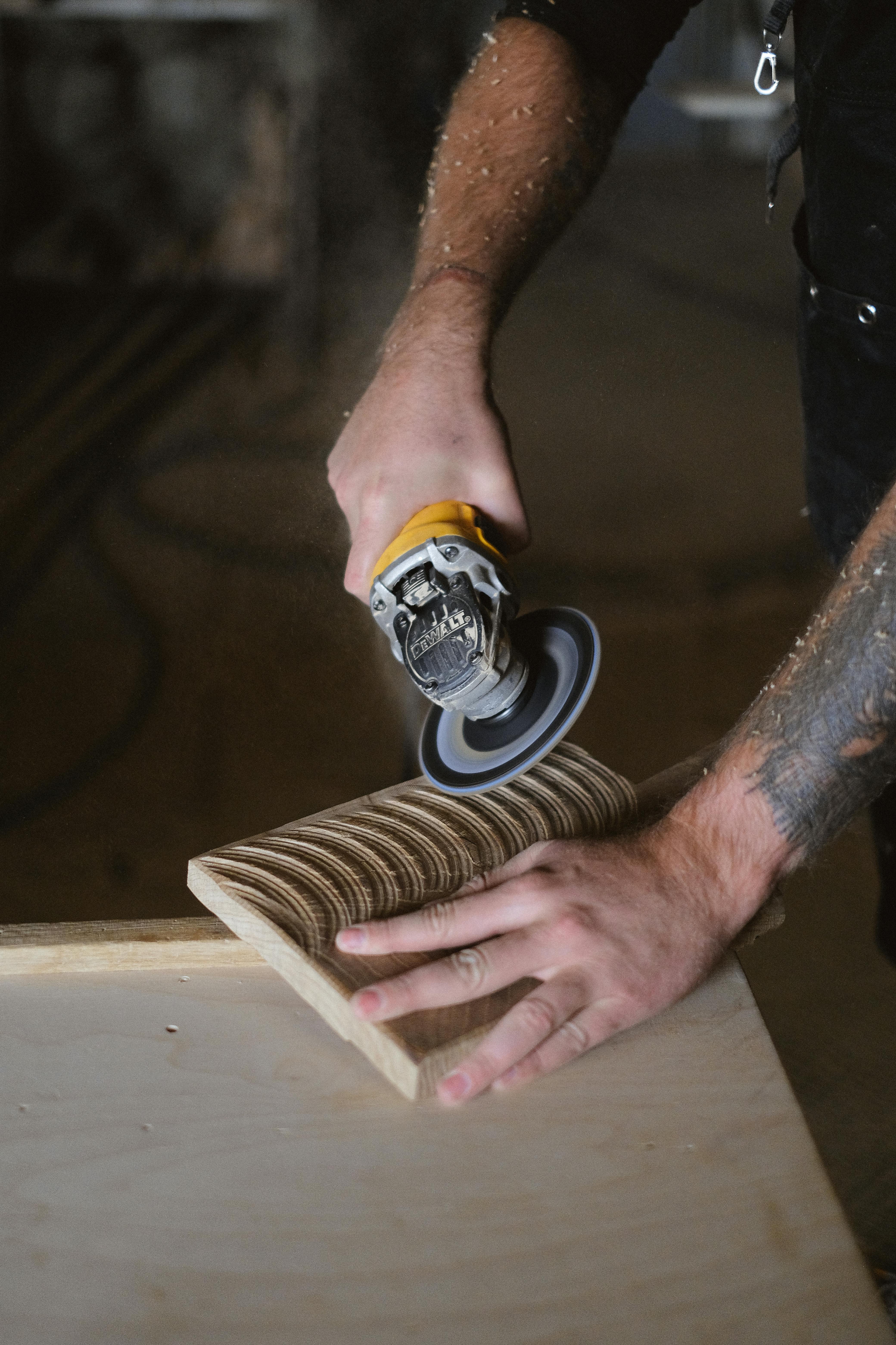 Crop craftsman creating patterns on wooden board with angle grinder ...