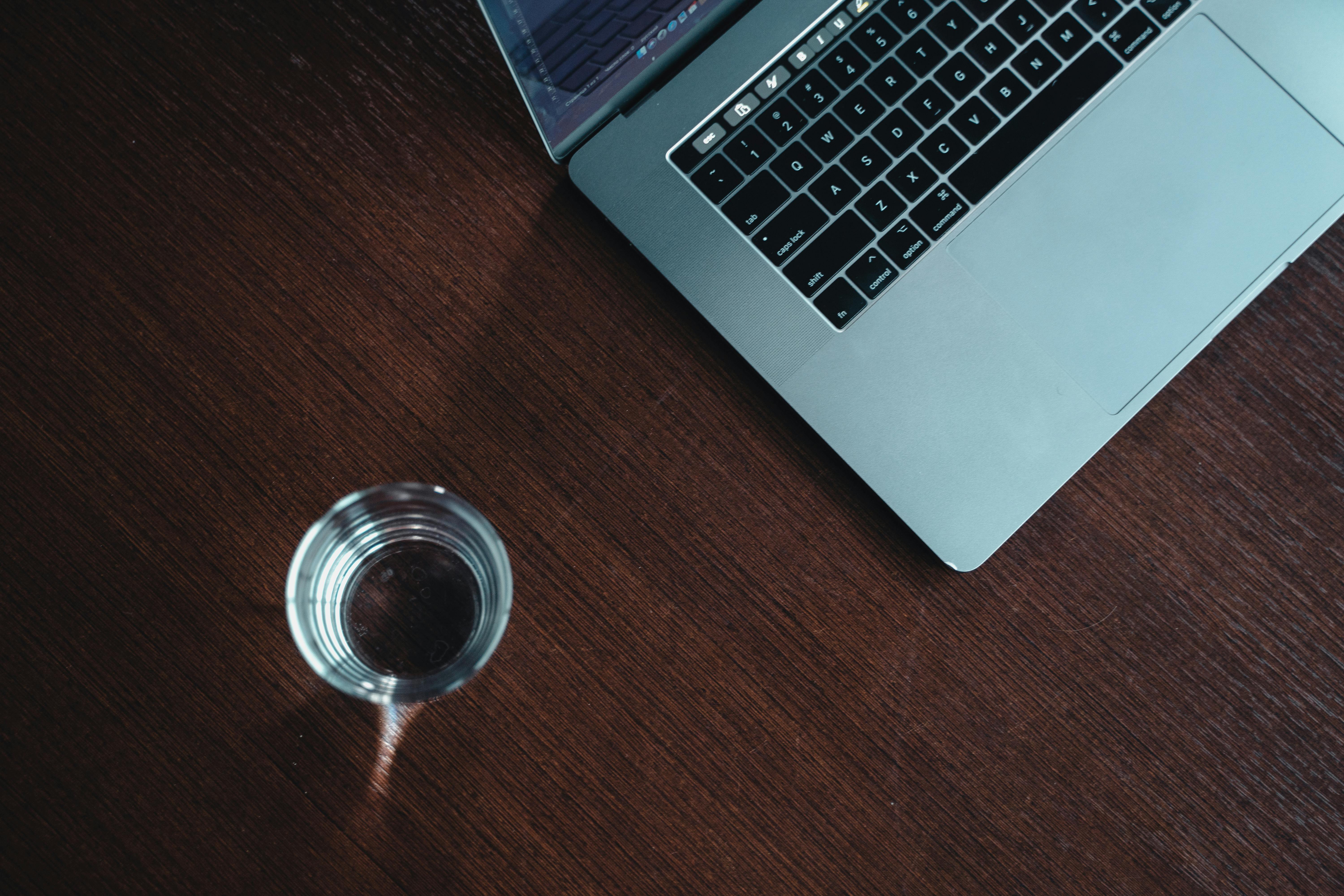 Laptop and Glass of Water on Brown Wooden Table · Free Stock Photo