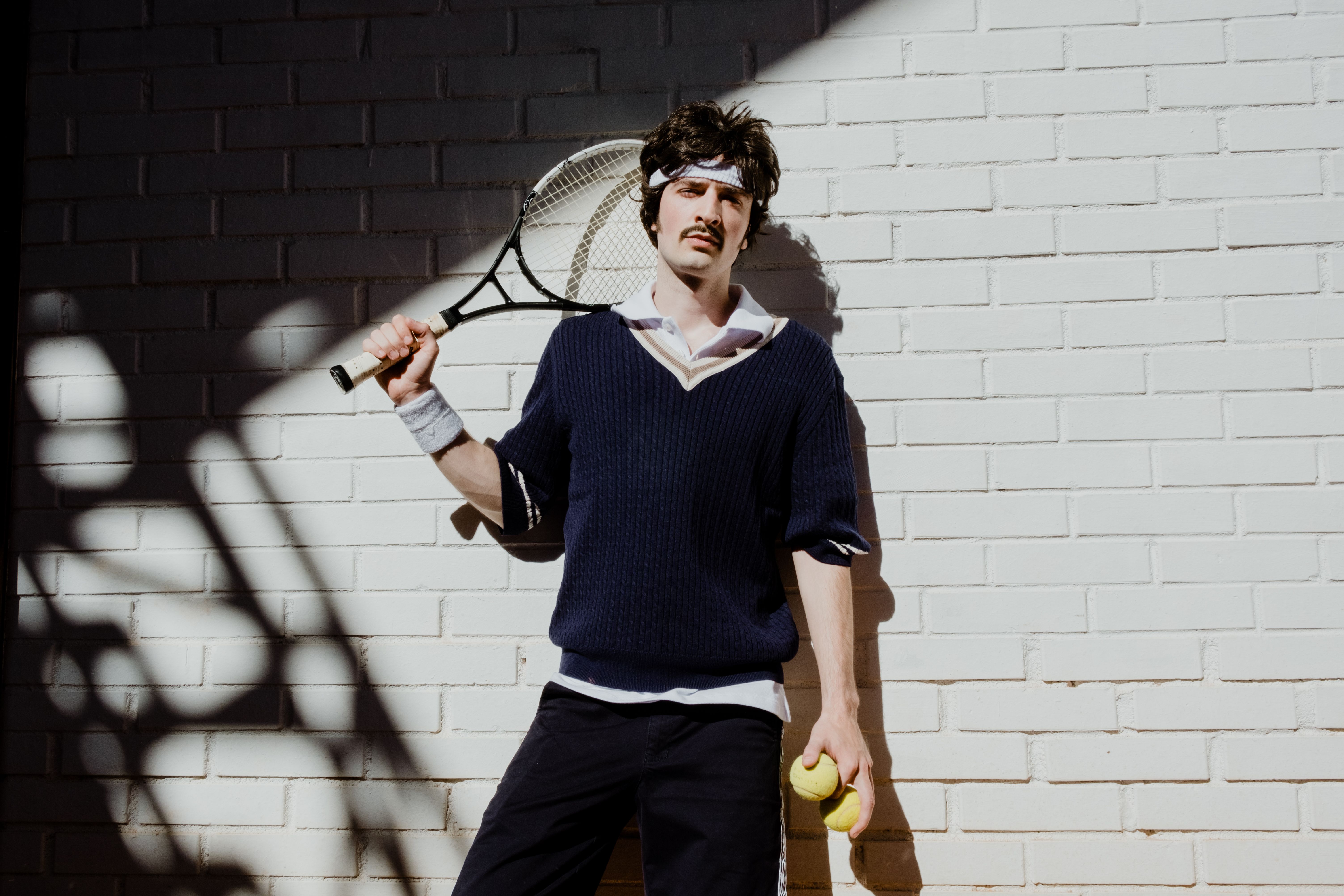 A Man Holding a Tennis Racket Sitting by a Brick Wall · Free Stock Photo