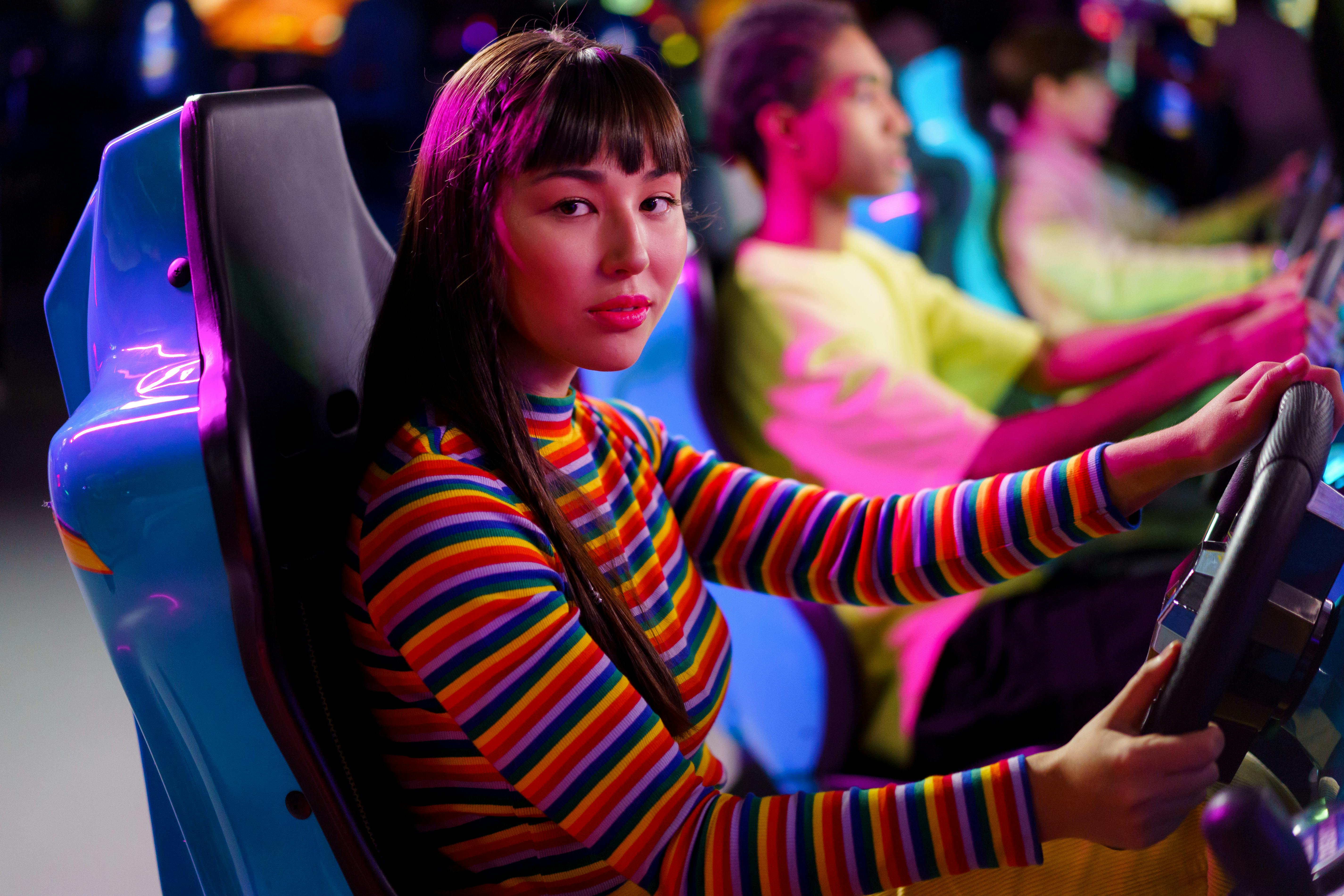 A Woman in Striped Long Sleeves Sitting on a Car Arcade Machine while ...