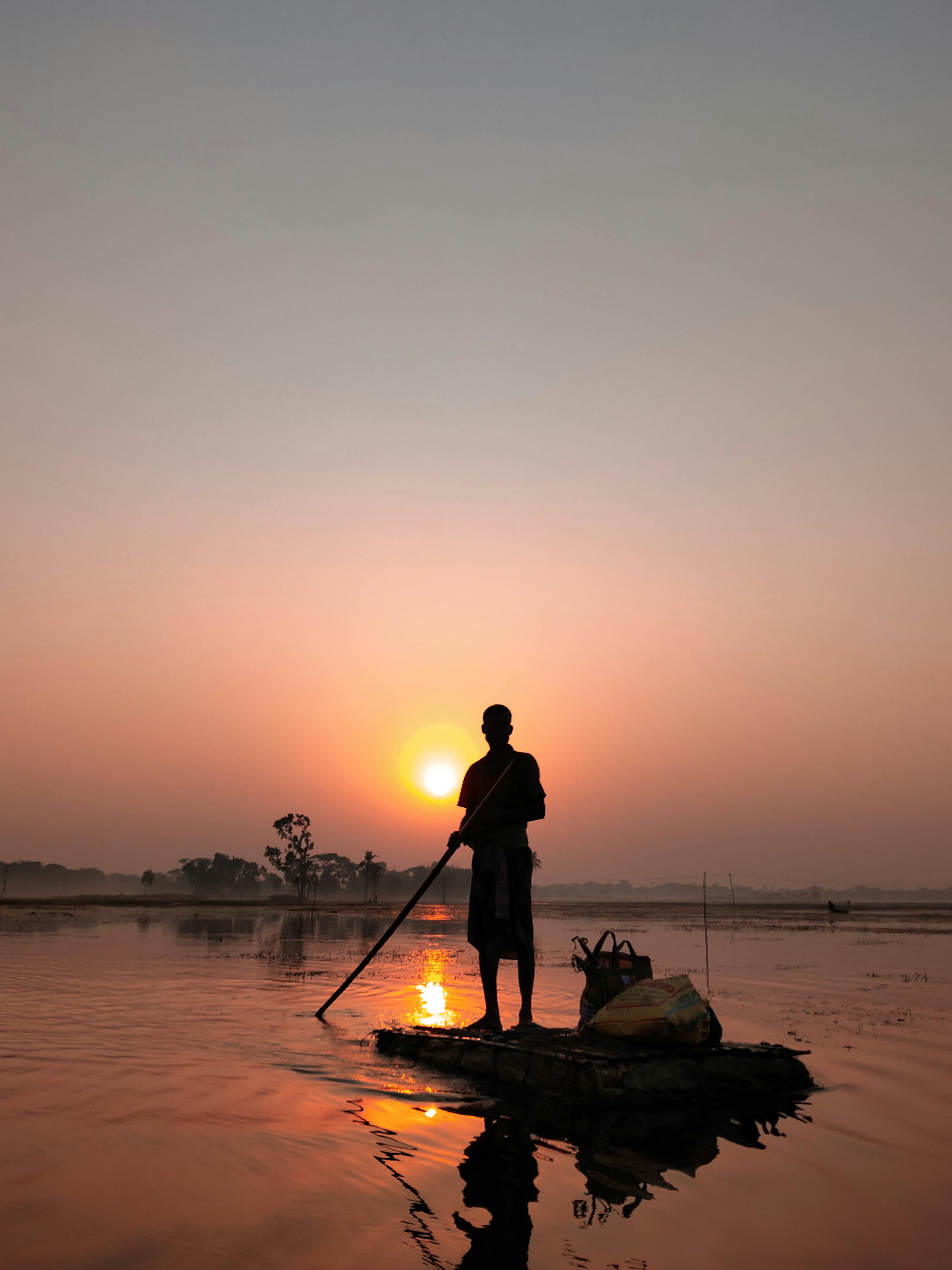 Silhouette of Man Standing on a Raft during Sunset · Free Stock Photo