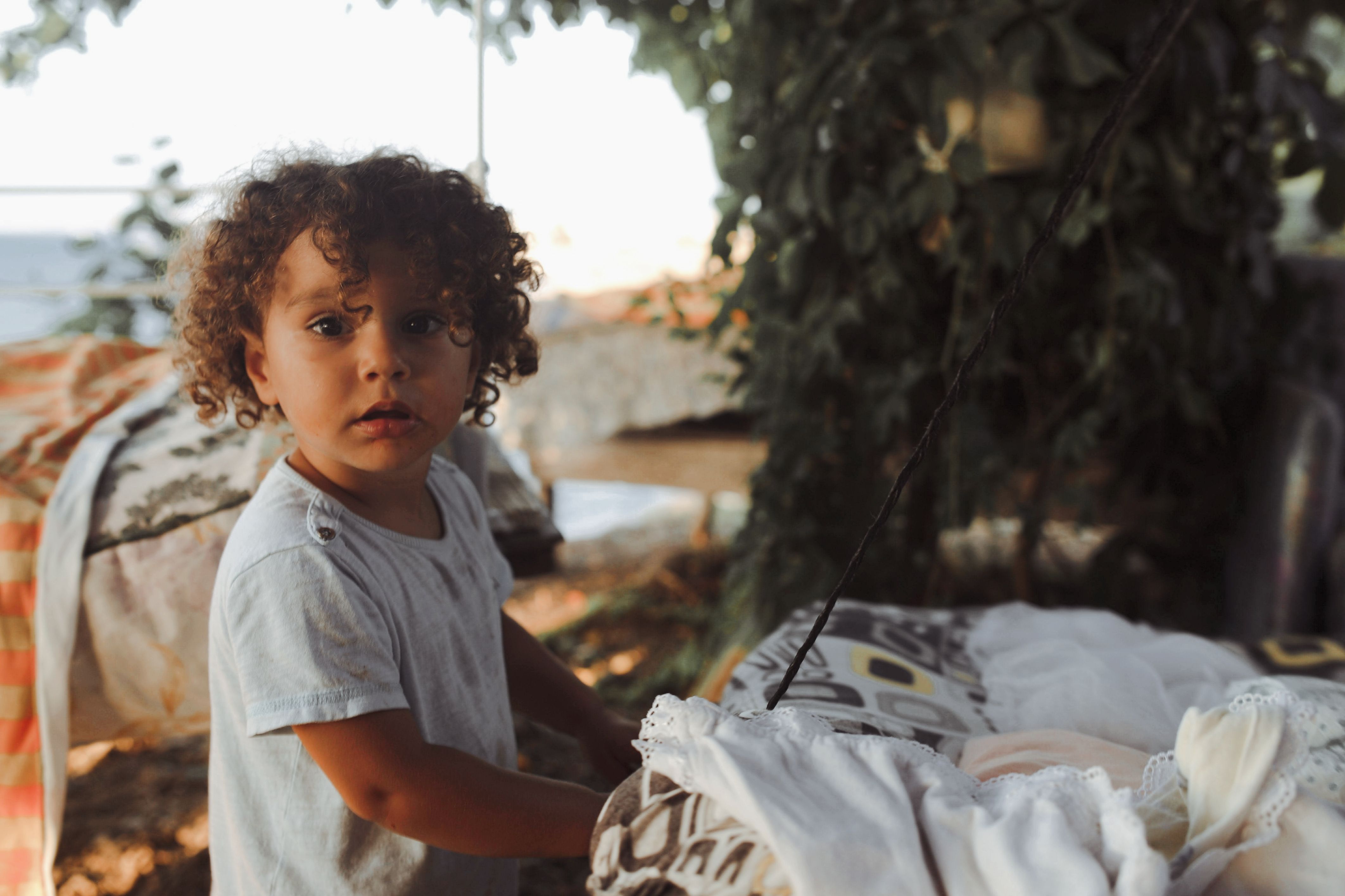 Cute ethnic child near soft fabrics in garden · Free Stock Photo