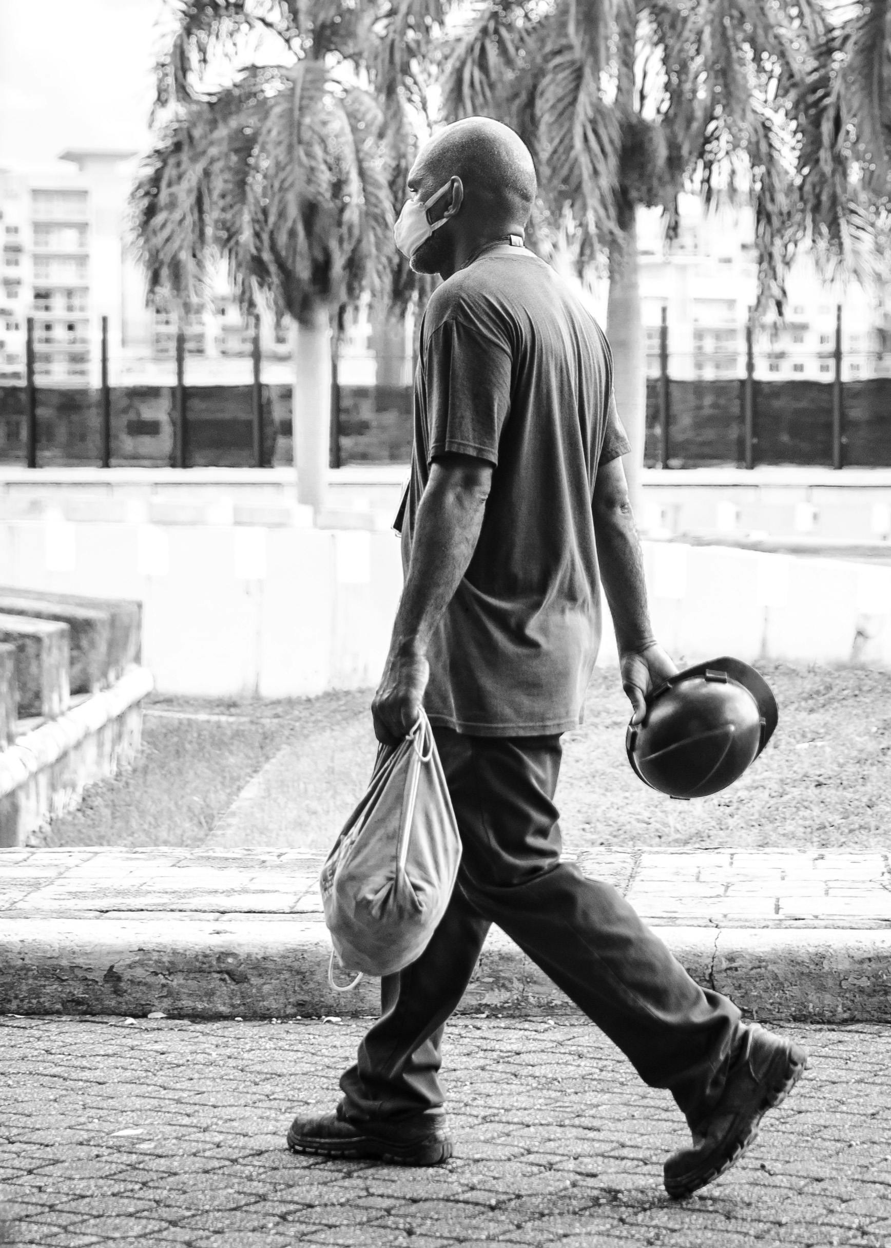 Man Walking on Stone Pavement with a Bag and Hard Hat · Free Stock Photo