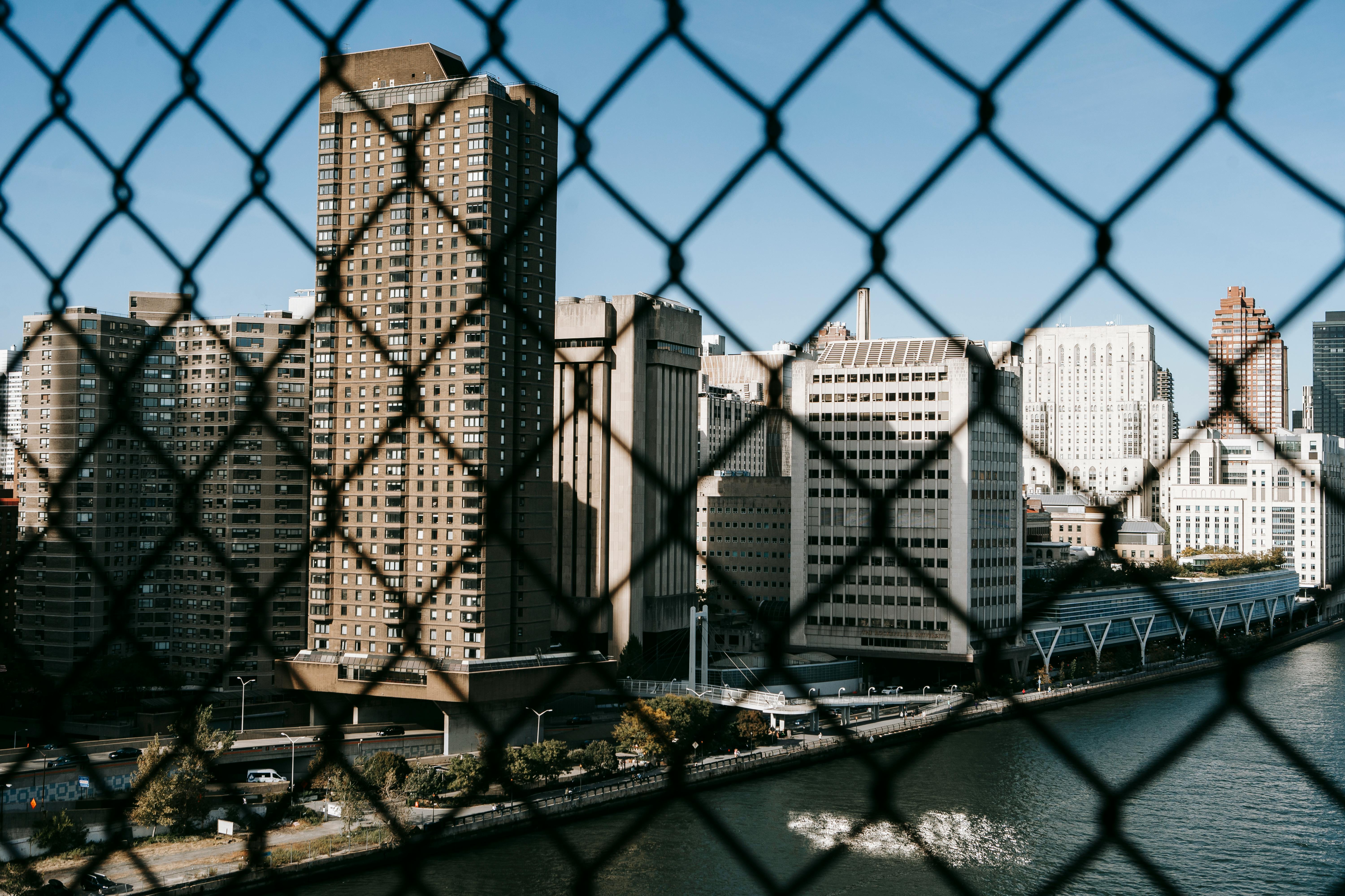 Modern city with tall buildings through metal chain link · Free Stock Photo