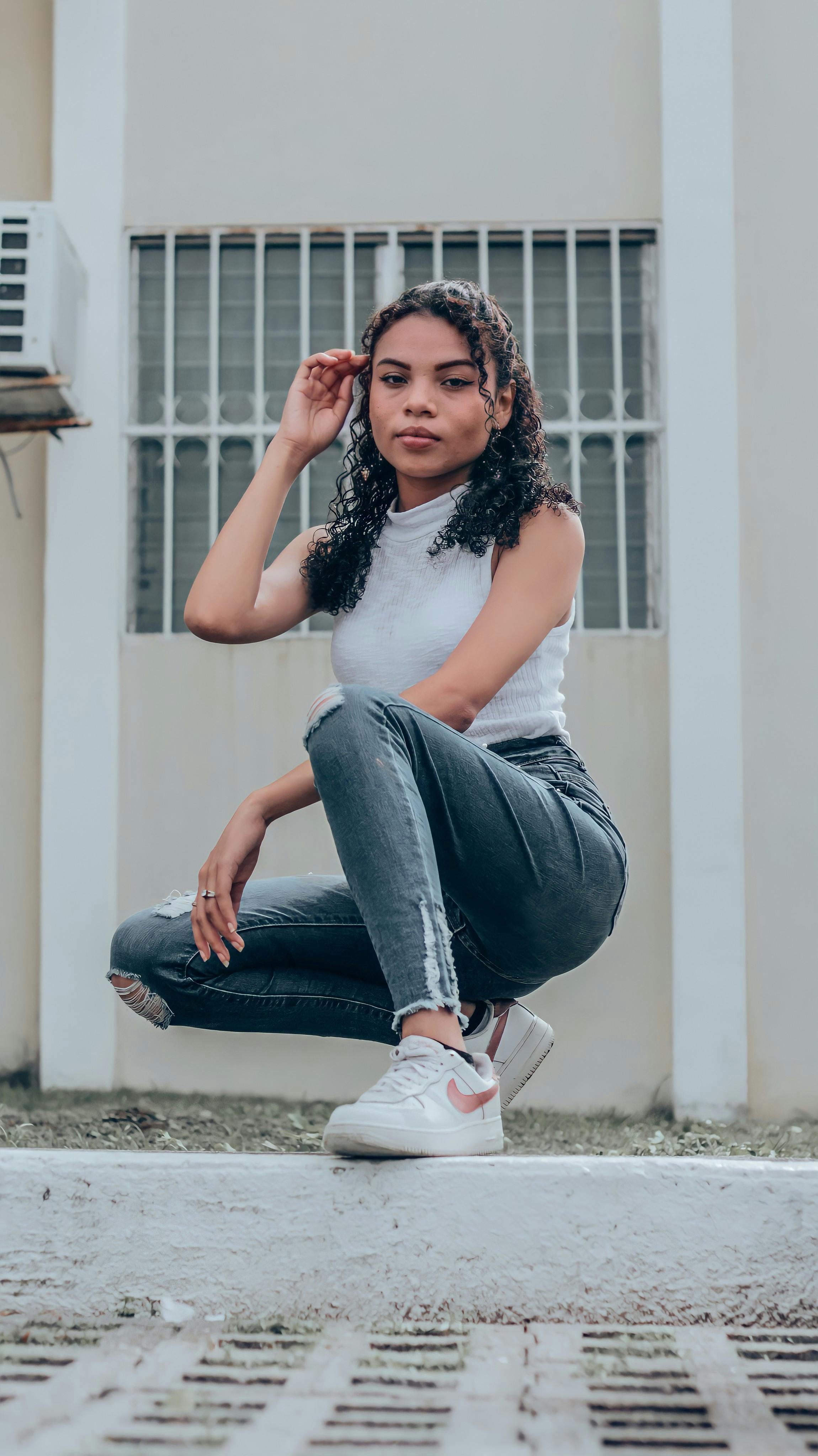 Portrait of Curly Haired Woman in Jeans Crouching · Free Stock Photo