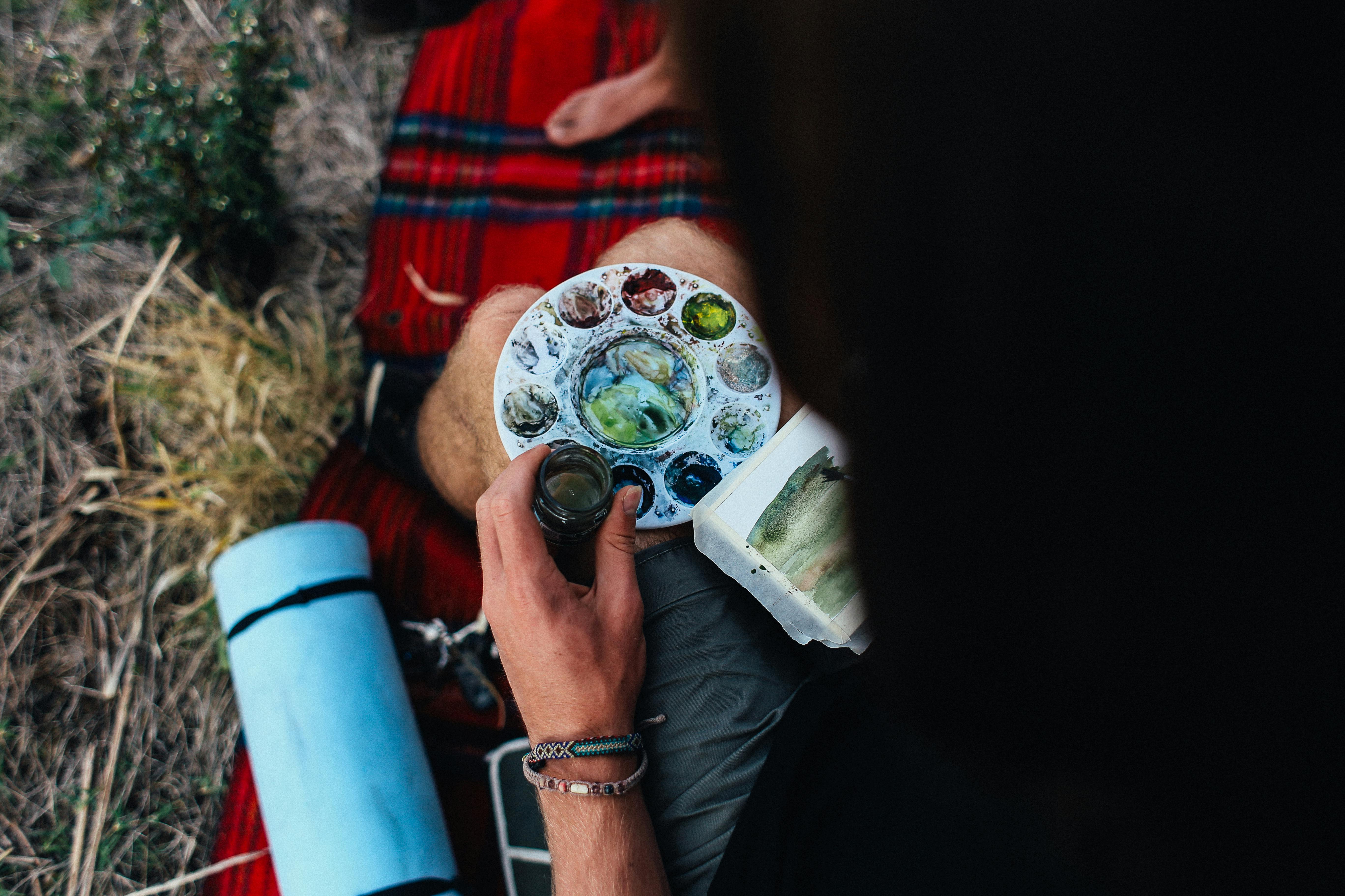Man Mixing Paint and Painting on a Mini Canvas Outdoors · Free Stock Photo