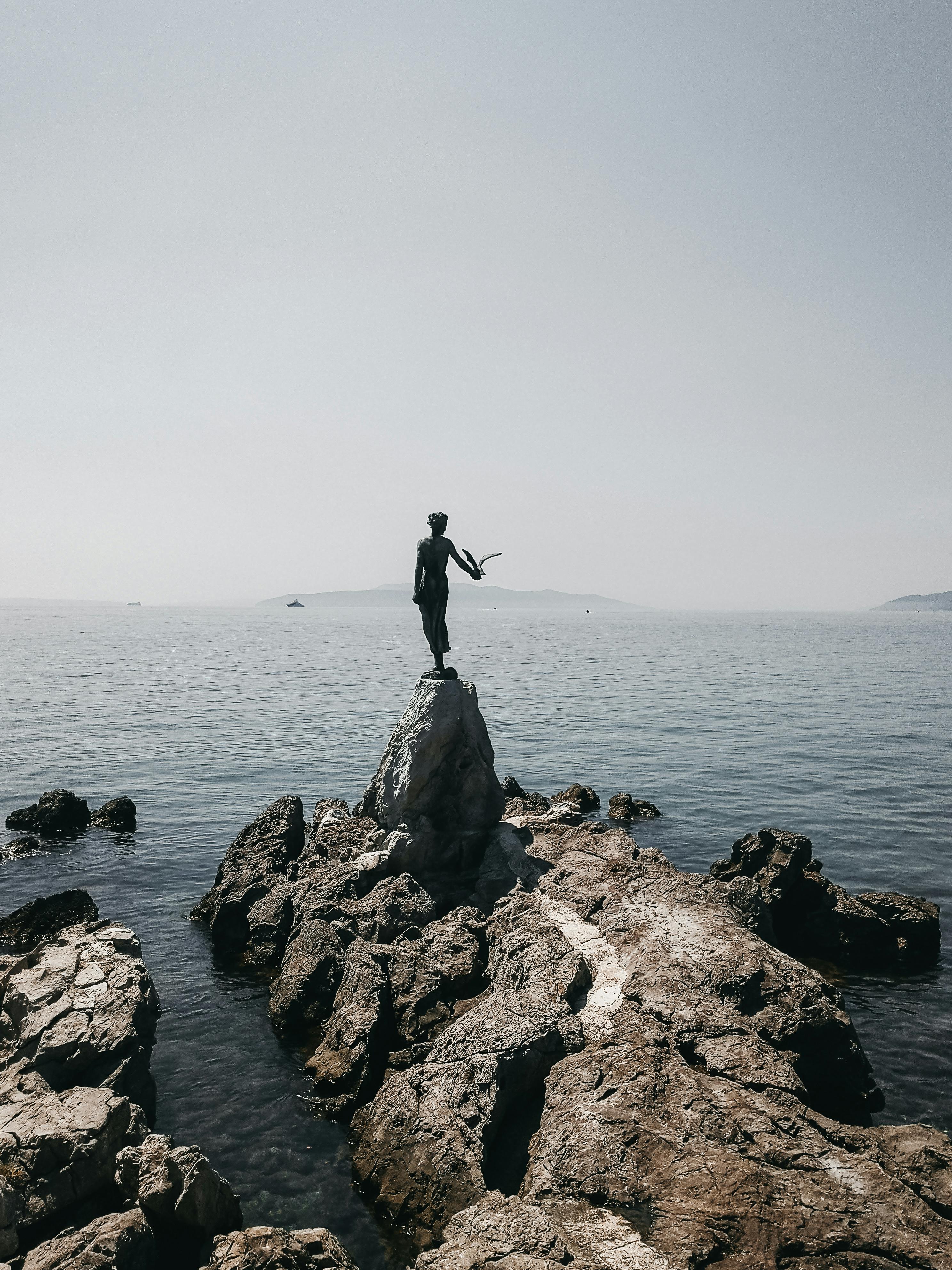 Woman statue on rocky cliff in sea · Free Stock Photo