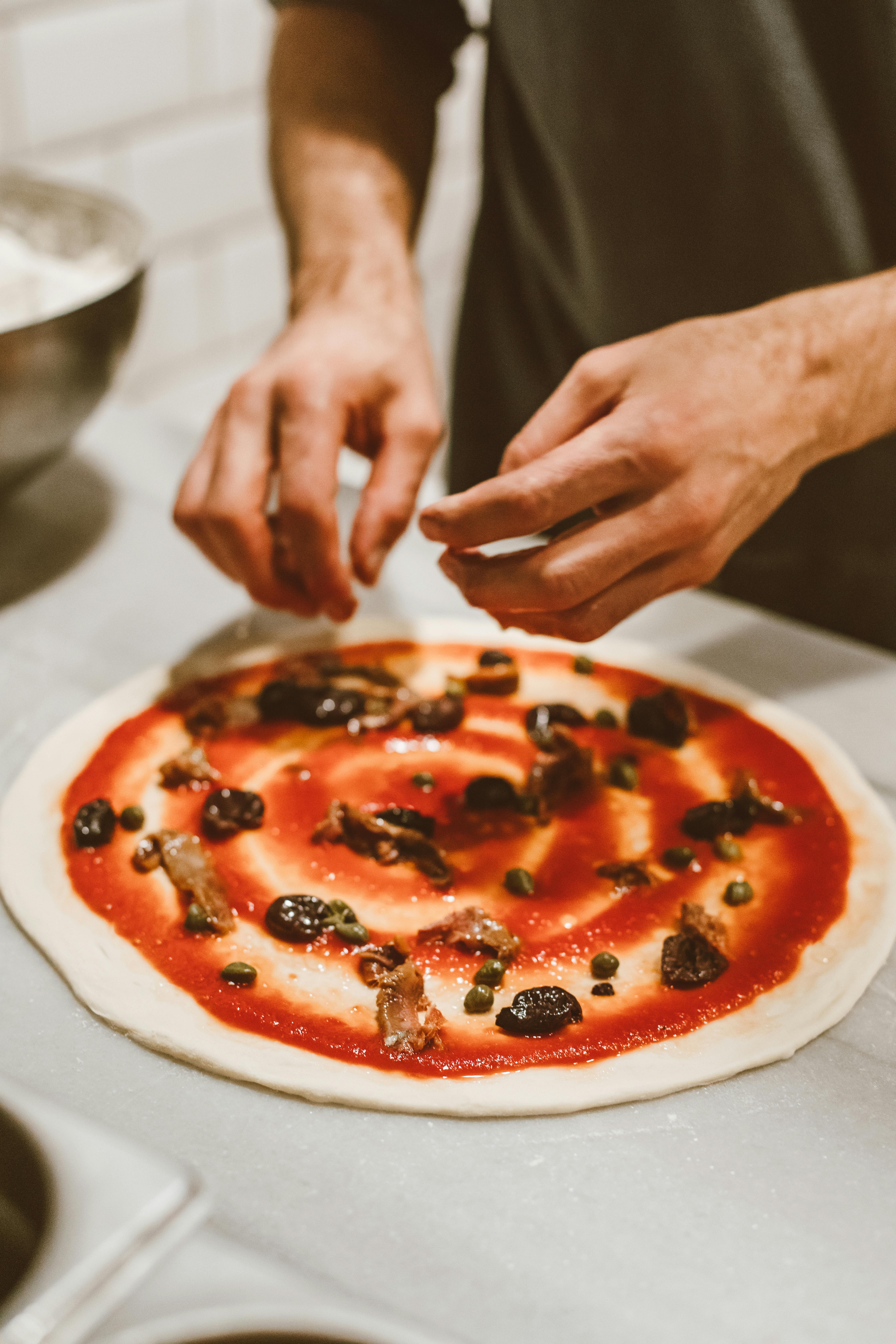 A Person Putting Toppings on a Dough with Tomato Sauce · Free Stock Photo