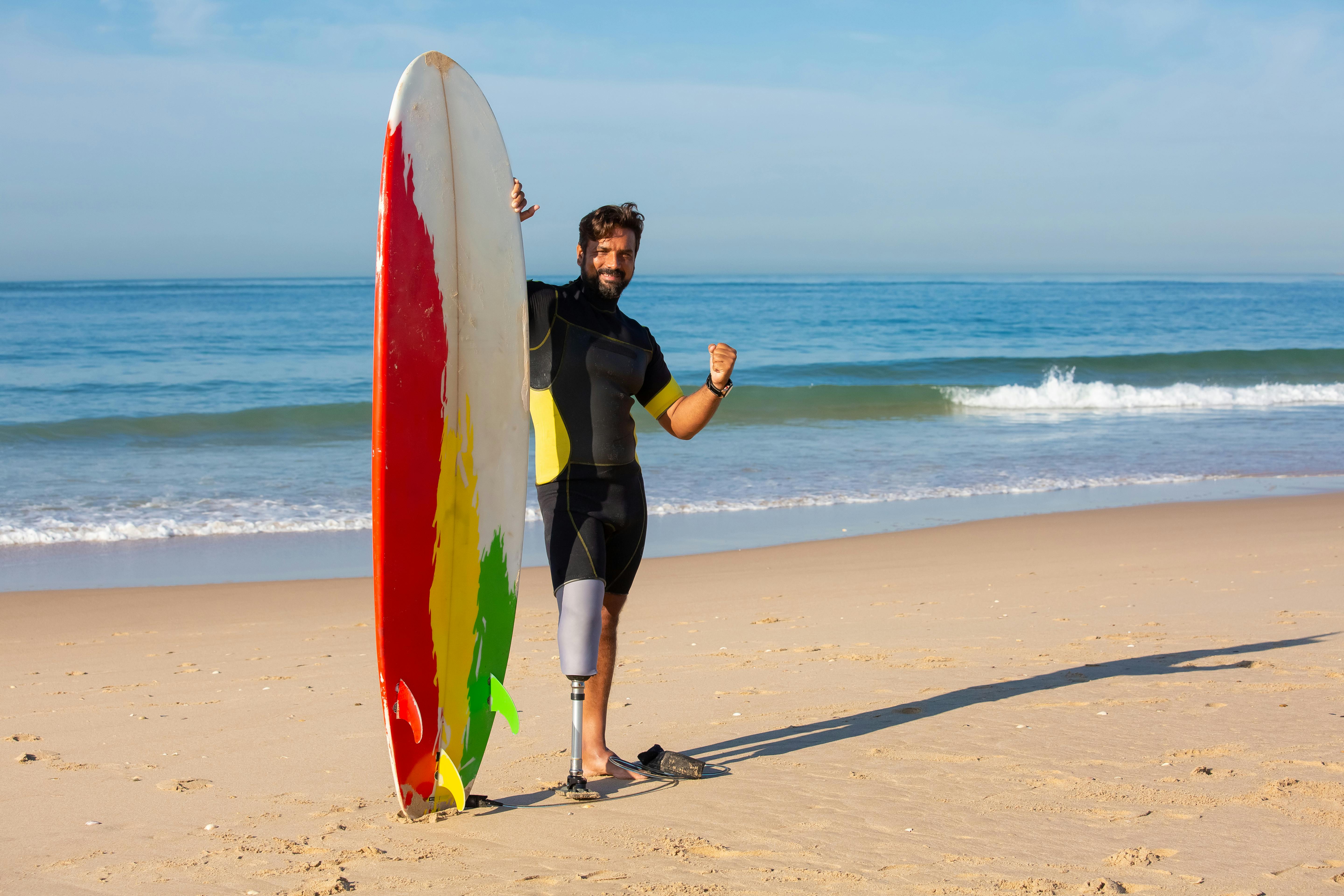 Content male surfer amputee standing near surfboard on sandy beach ...