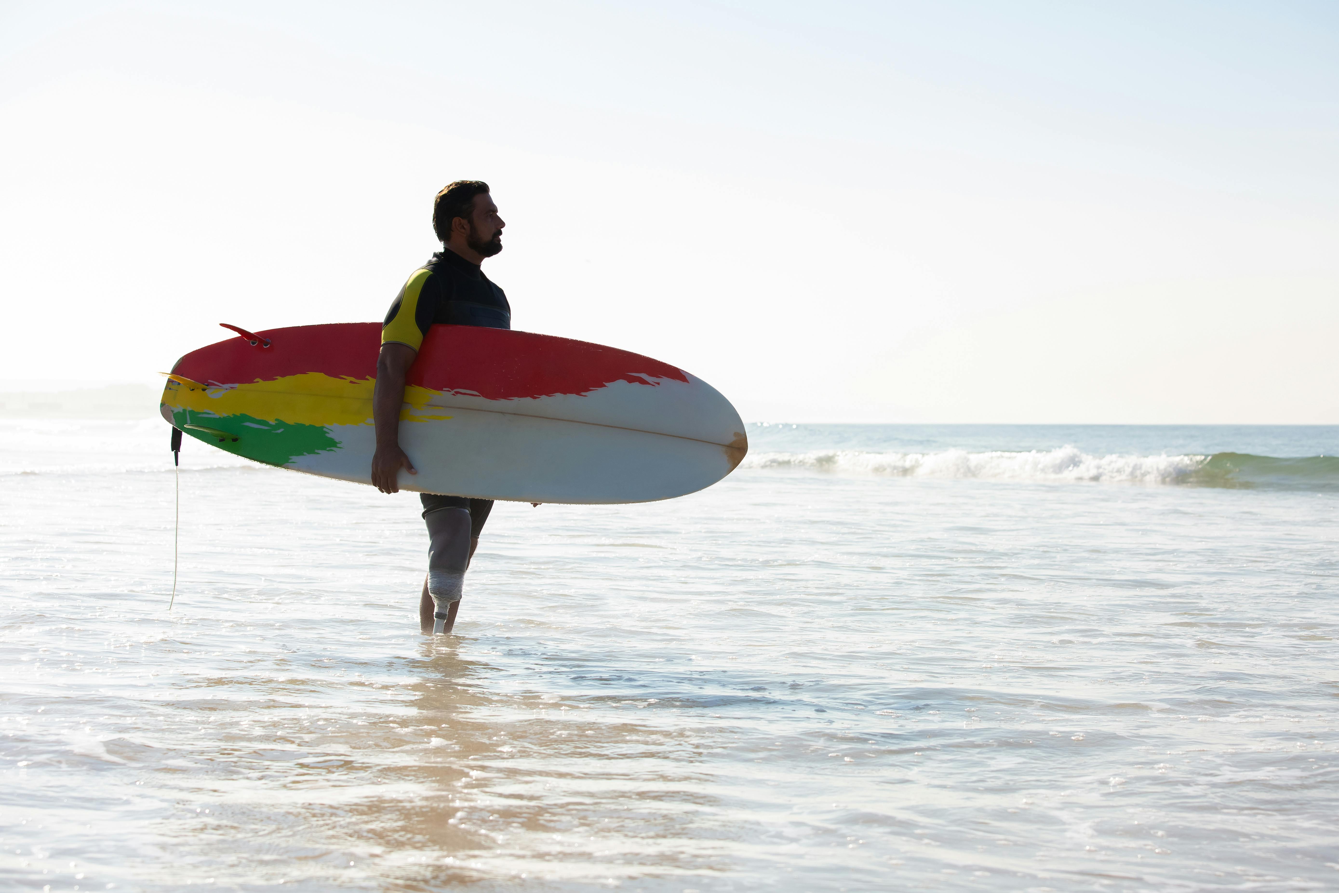 Male amputee surfer with surfboard standing in seawater · Free Stock Photo