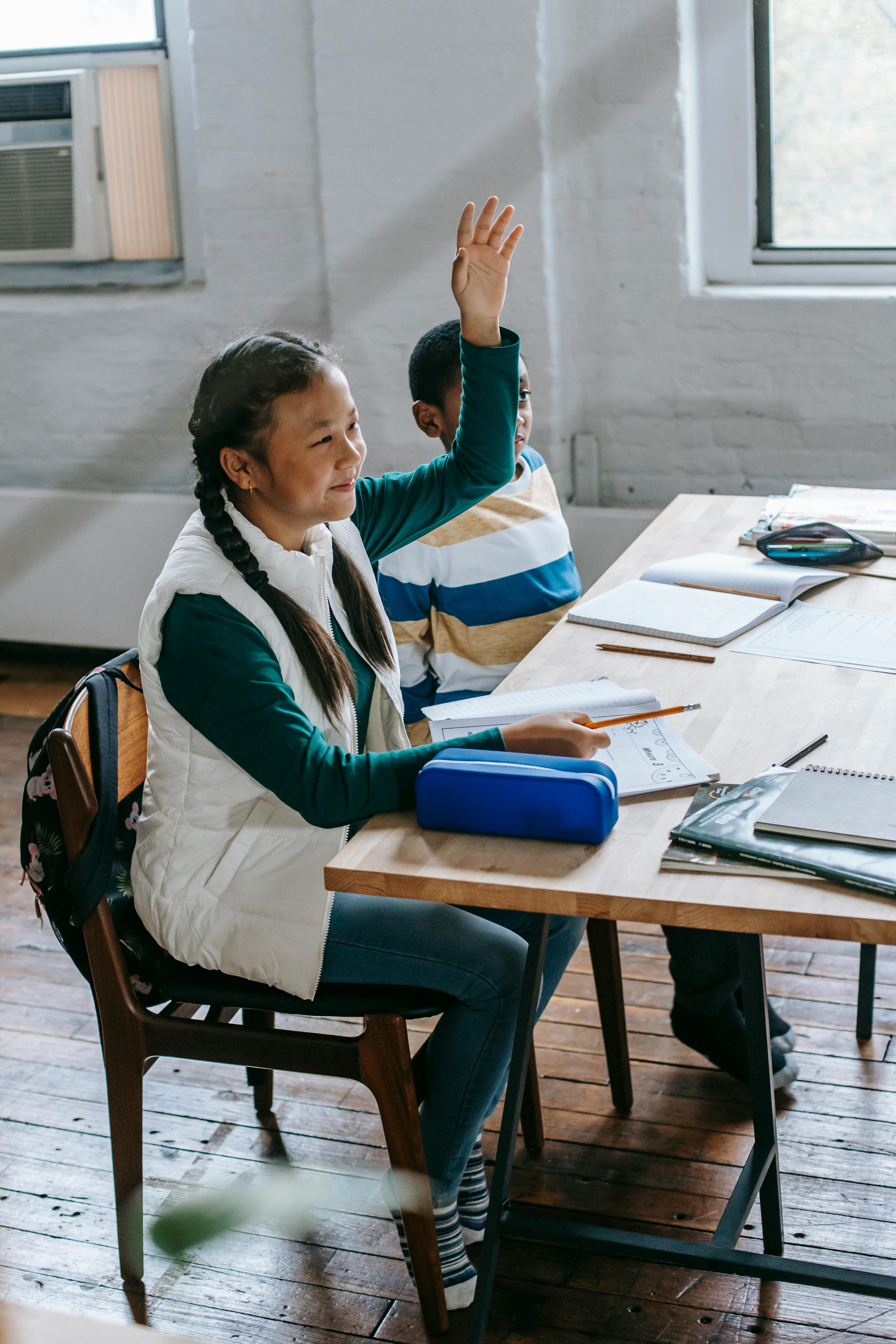 Cheerful Asian schoolgirl raising hand in classroom · Free Stock Photo