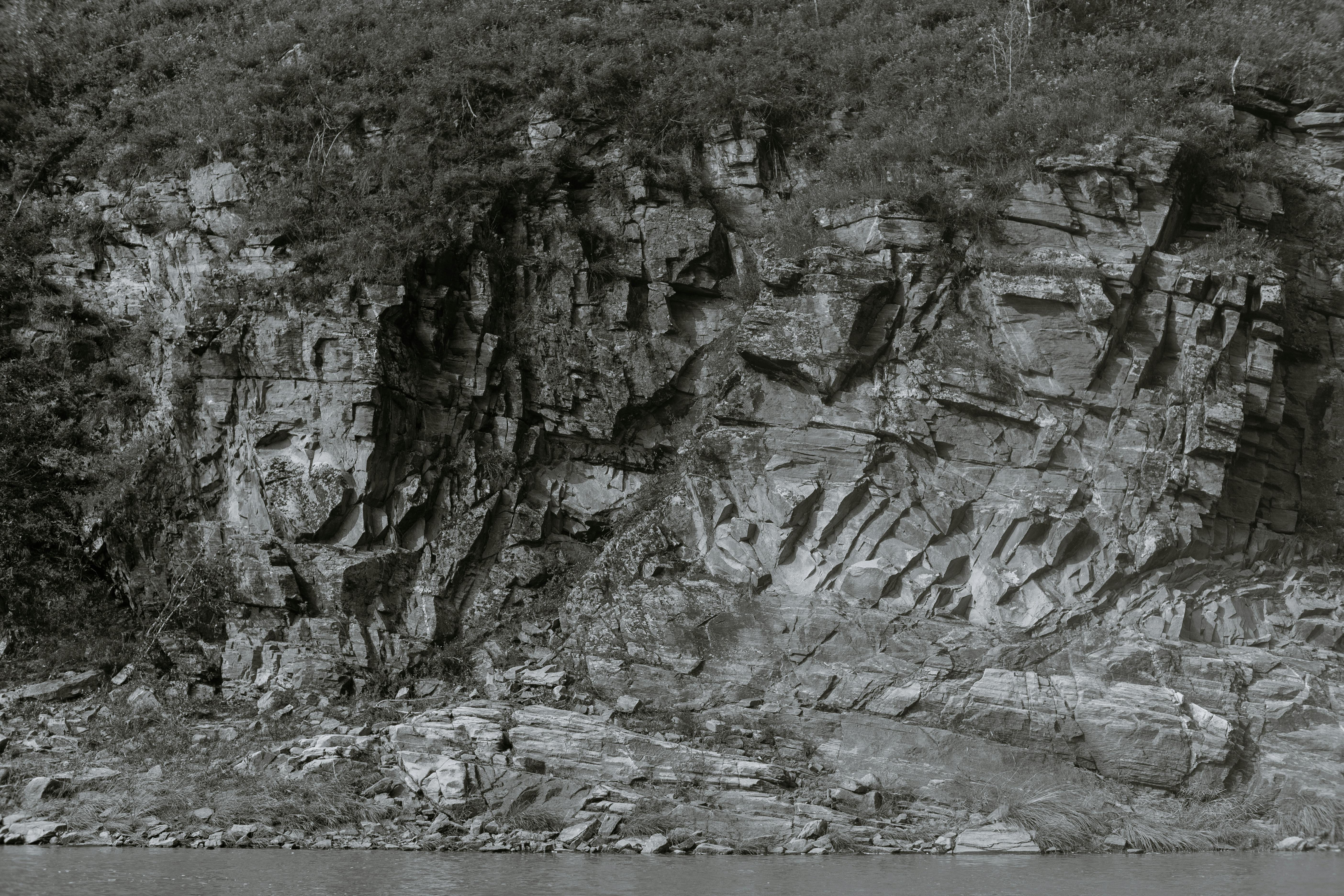 High rough rock with grass against lake · Free Stock Photo