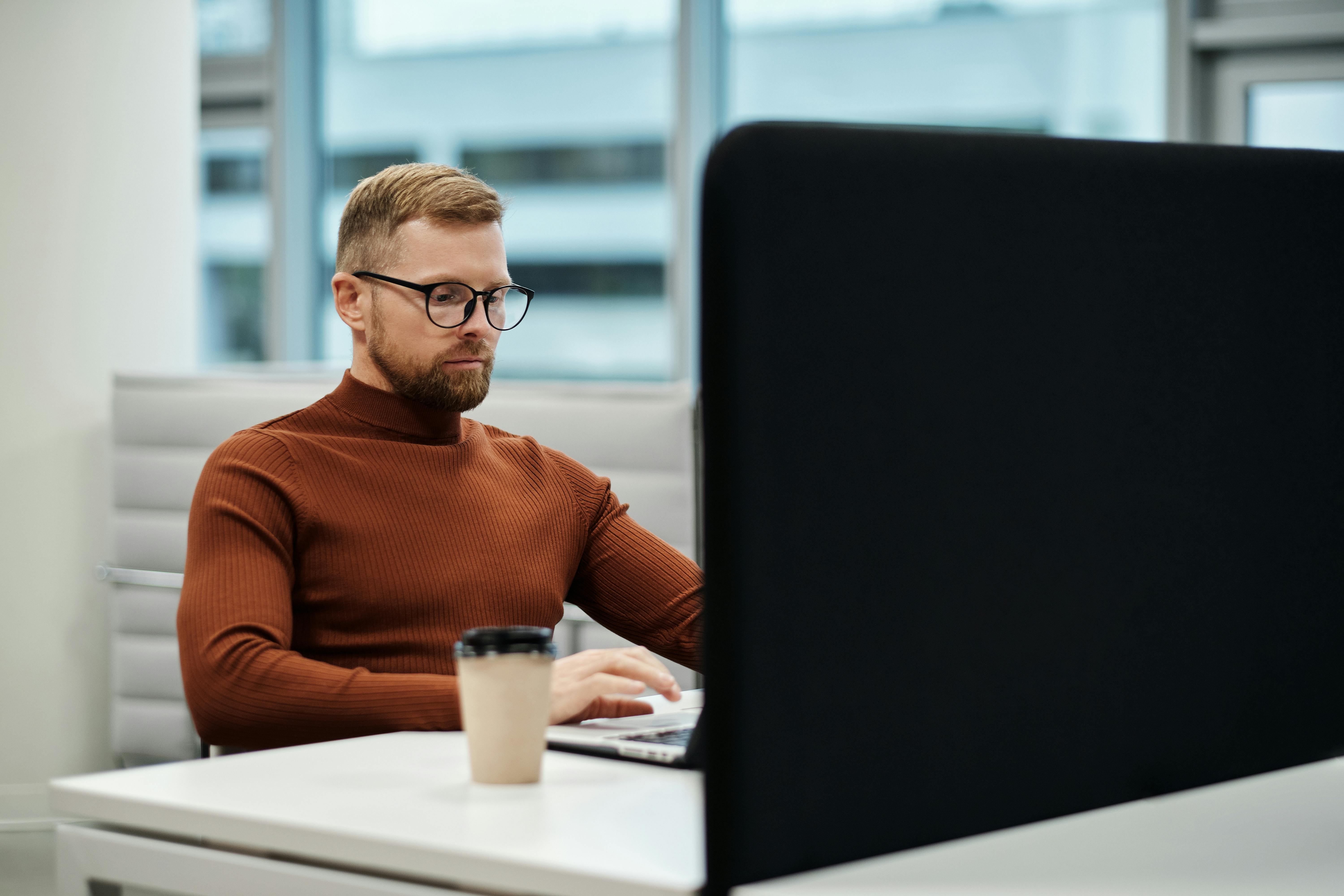 Man Wearing a Brown Sweater Sitting in an Office by a Large Computer ...