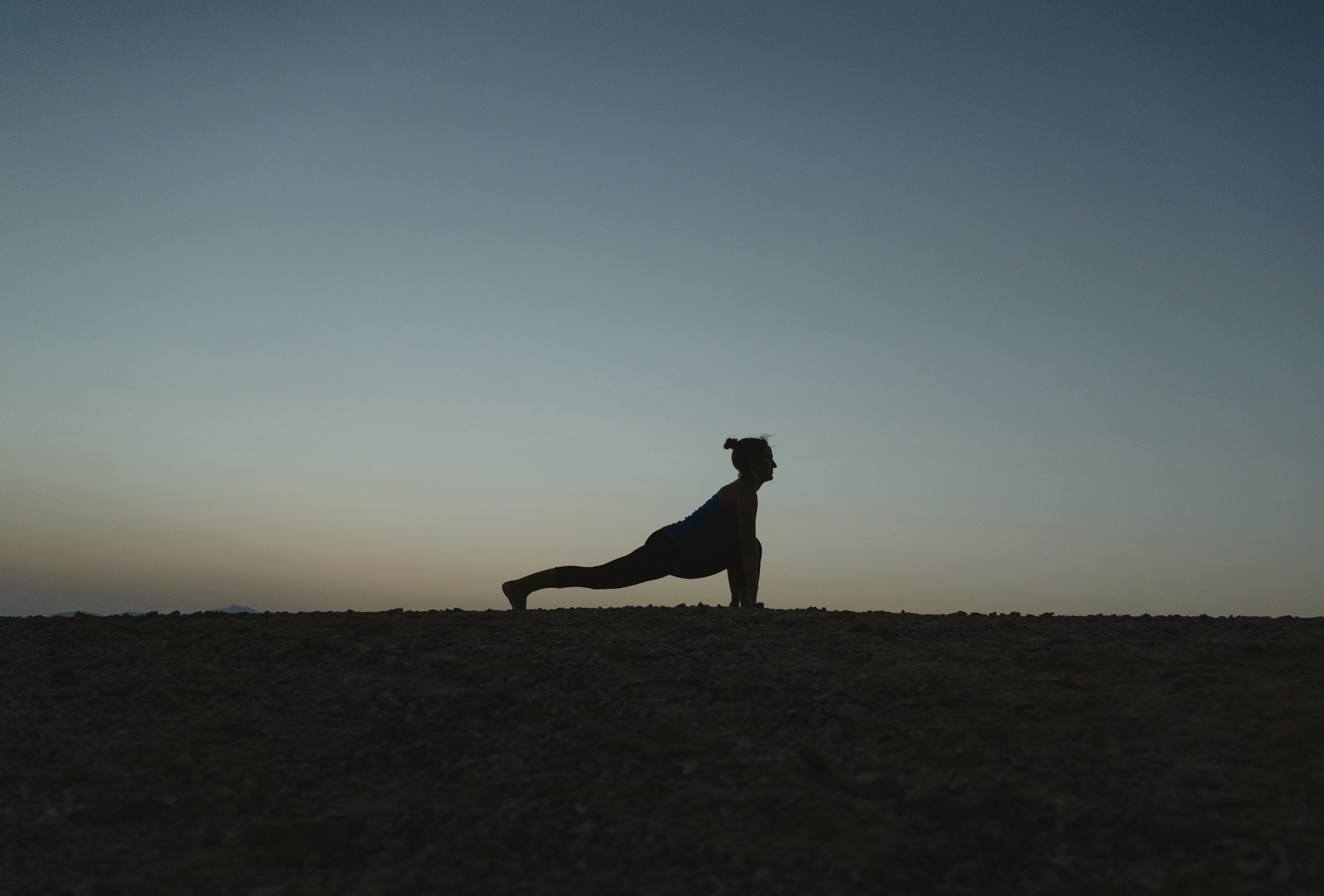 Silhouette of a Woman Doing Yoga Pose on he Ground During Sundown ...