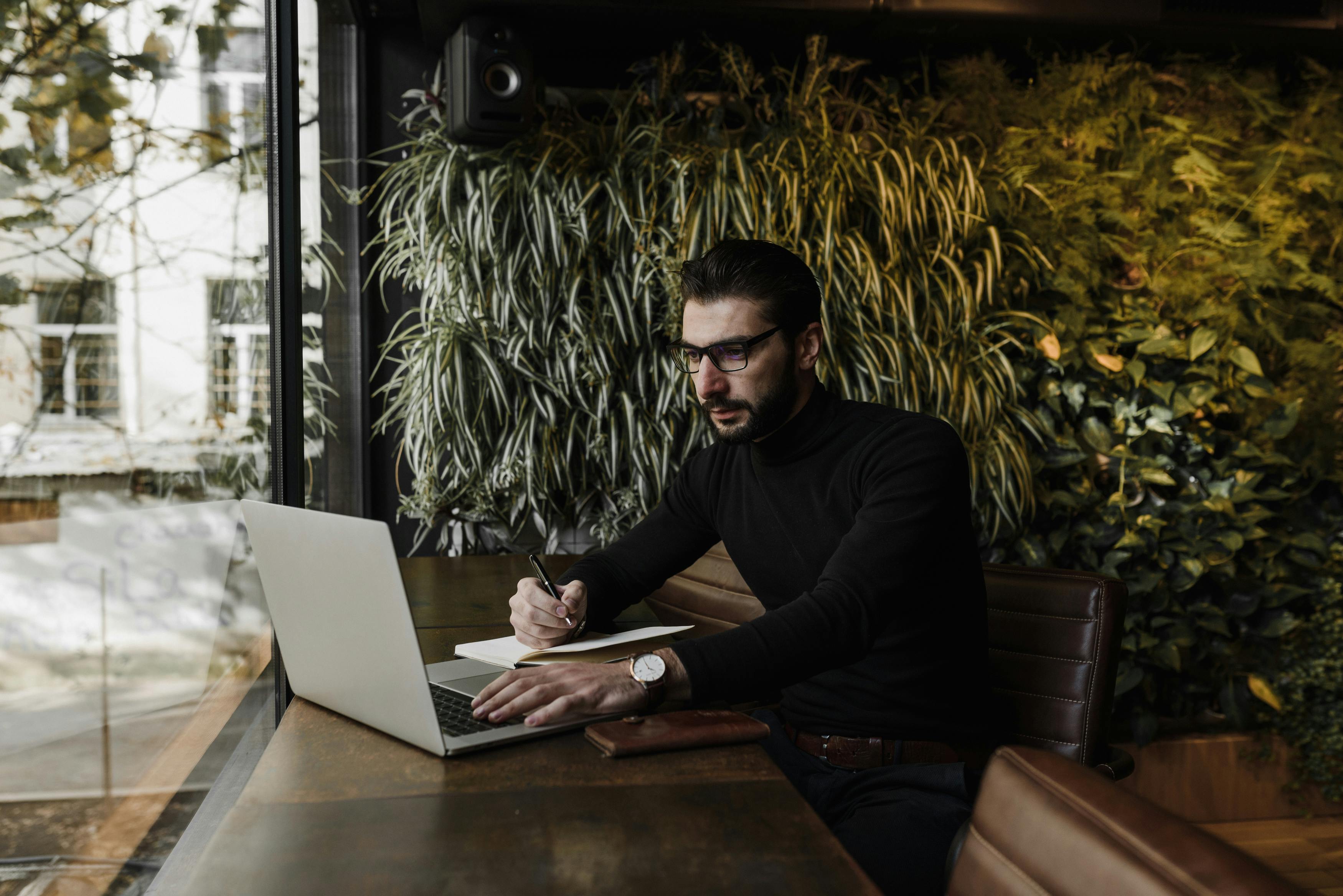 A Man using Laptop while Writing · Free Stock Photo