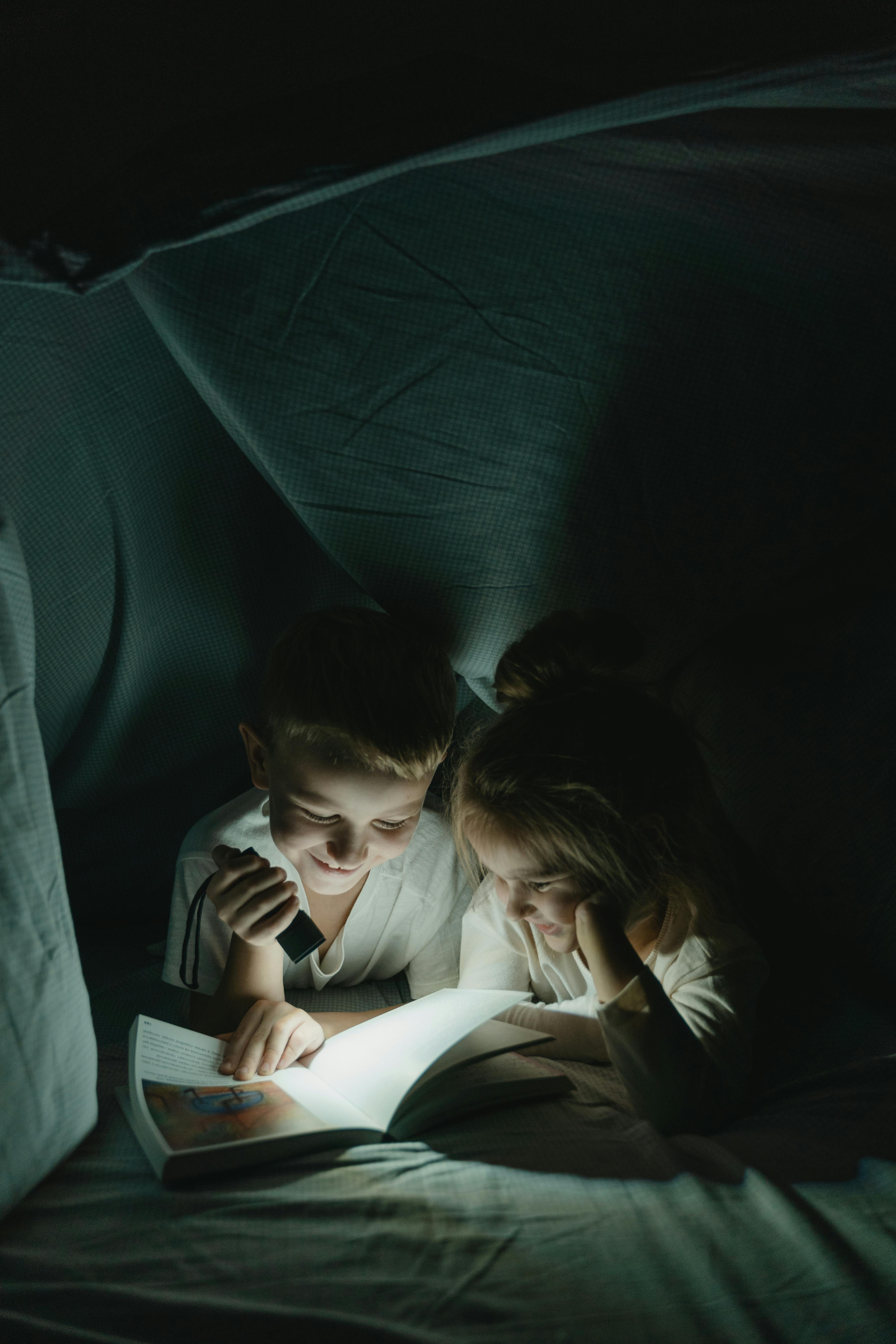 A Boy and Girl Reading a Book using Flashlight · Free Stock Photo