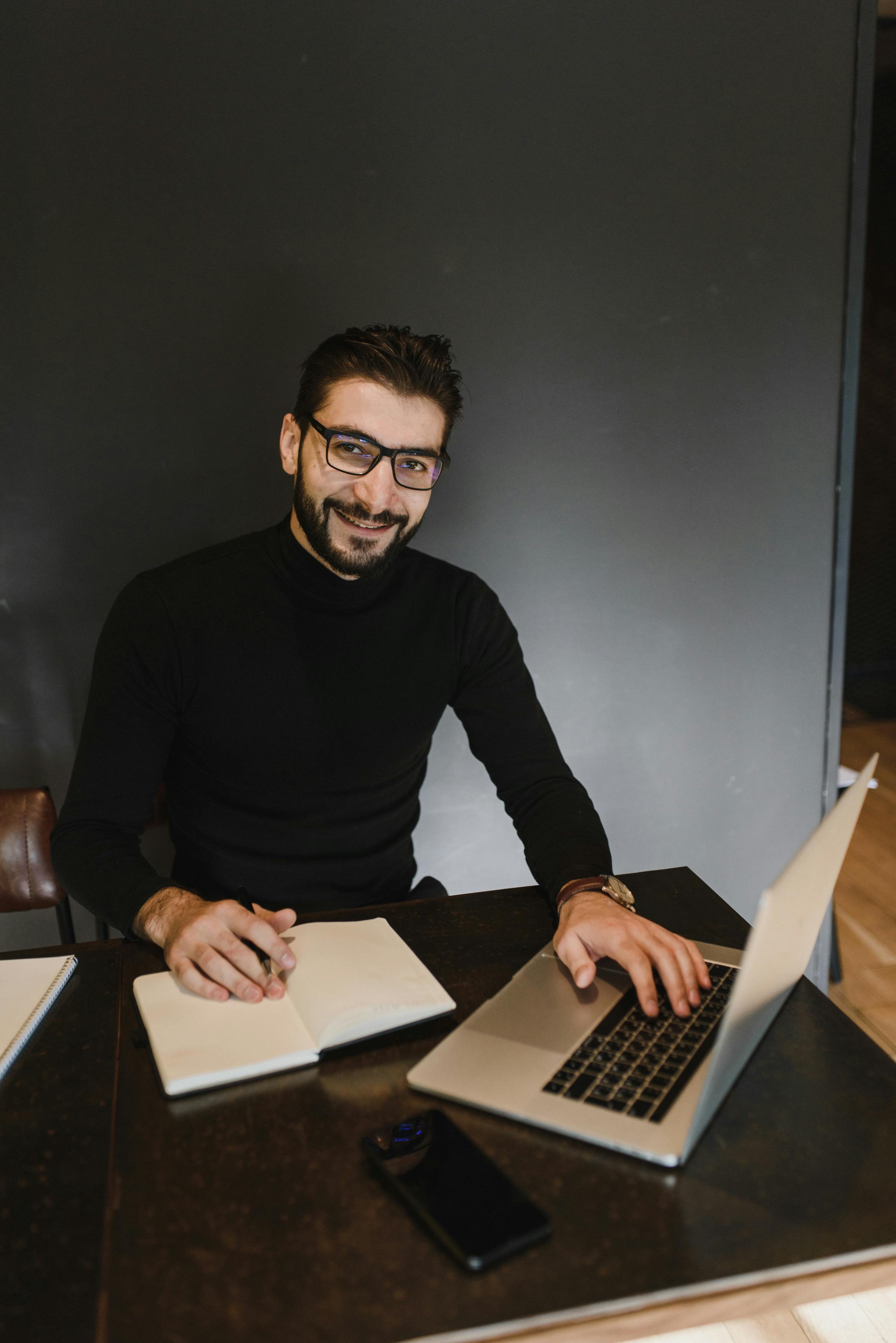 Focused Asian employee writing in diary at office desk · Free Stock Photo
