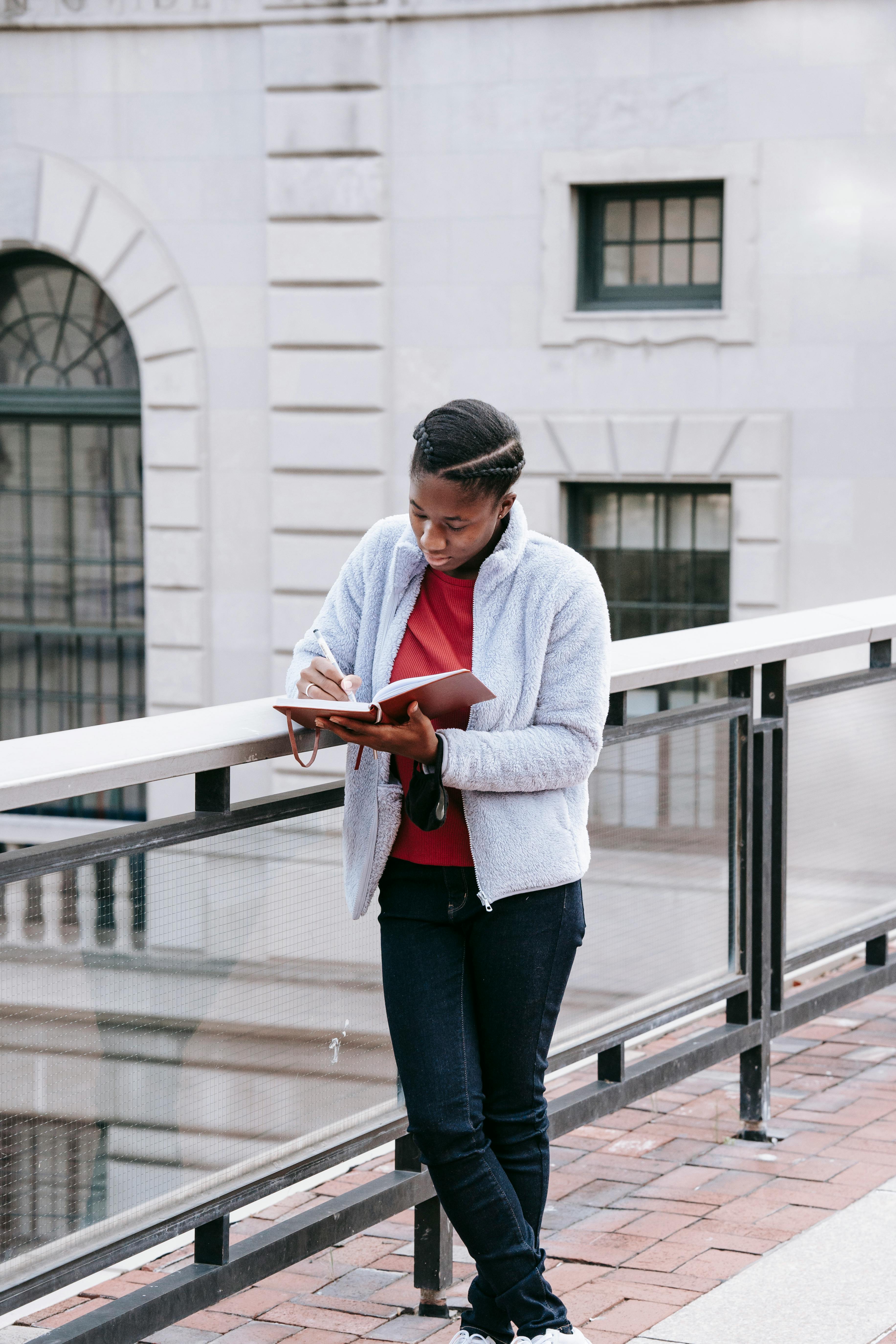 Attentive black student writing in diary on urban bridge · Free Stock Photo