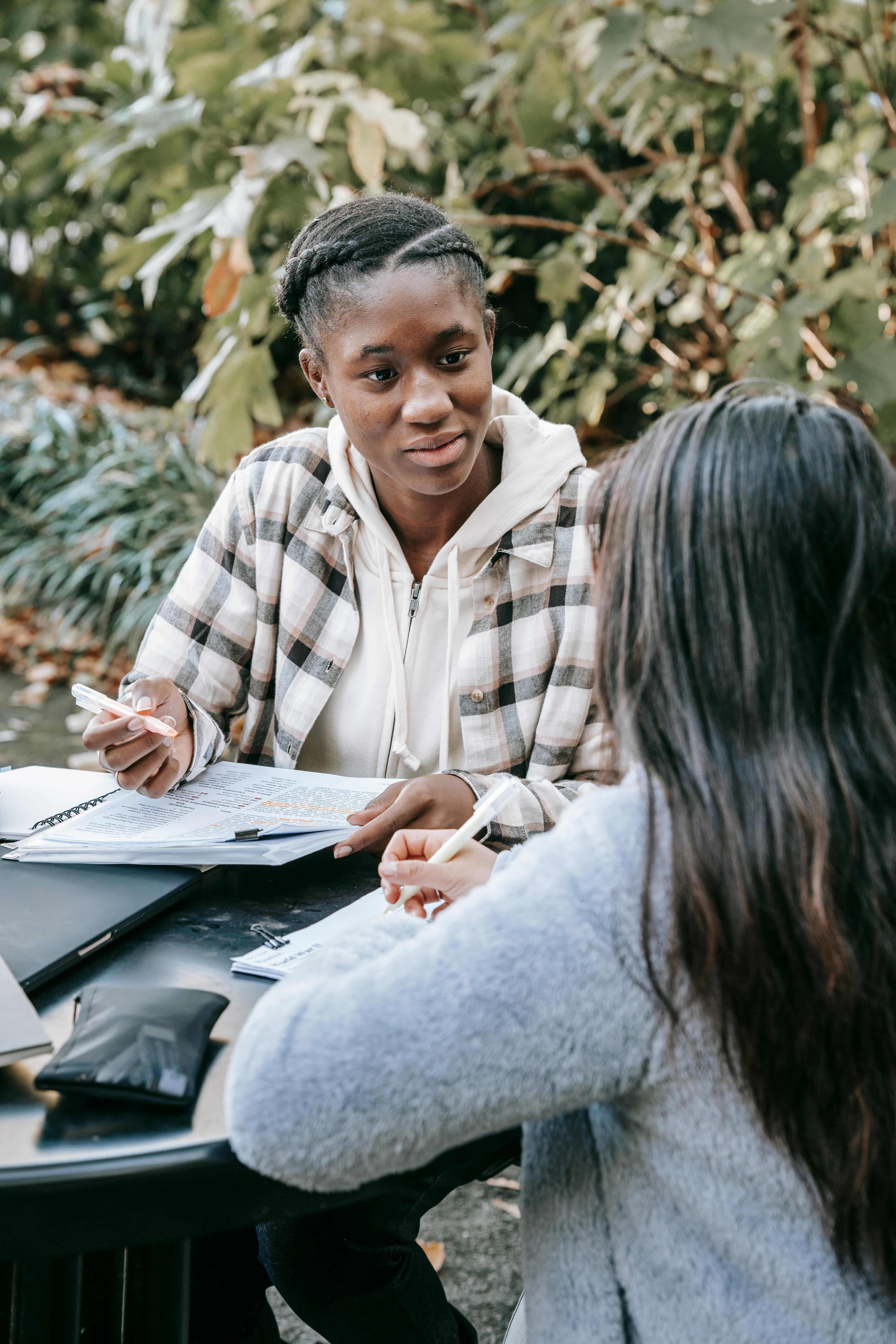 Positive multiethnic female students working on assignment in park ...
