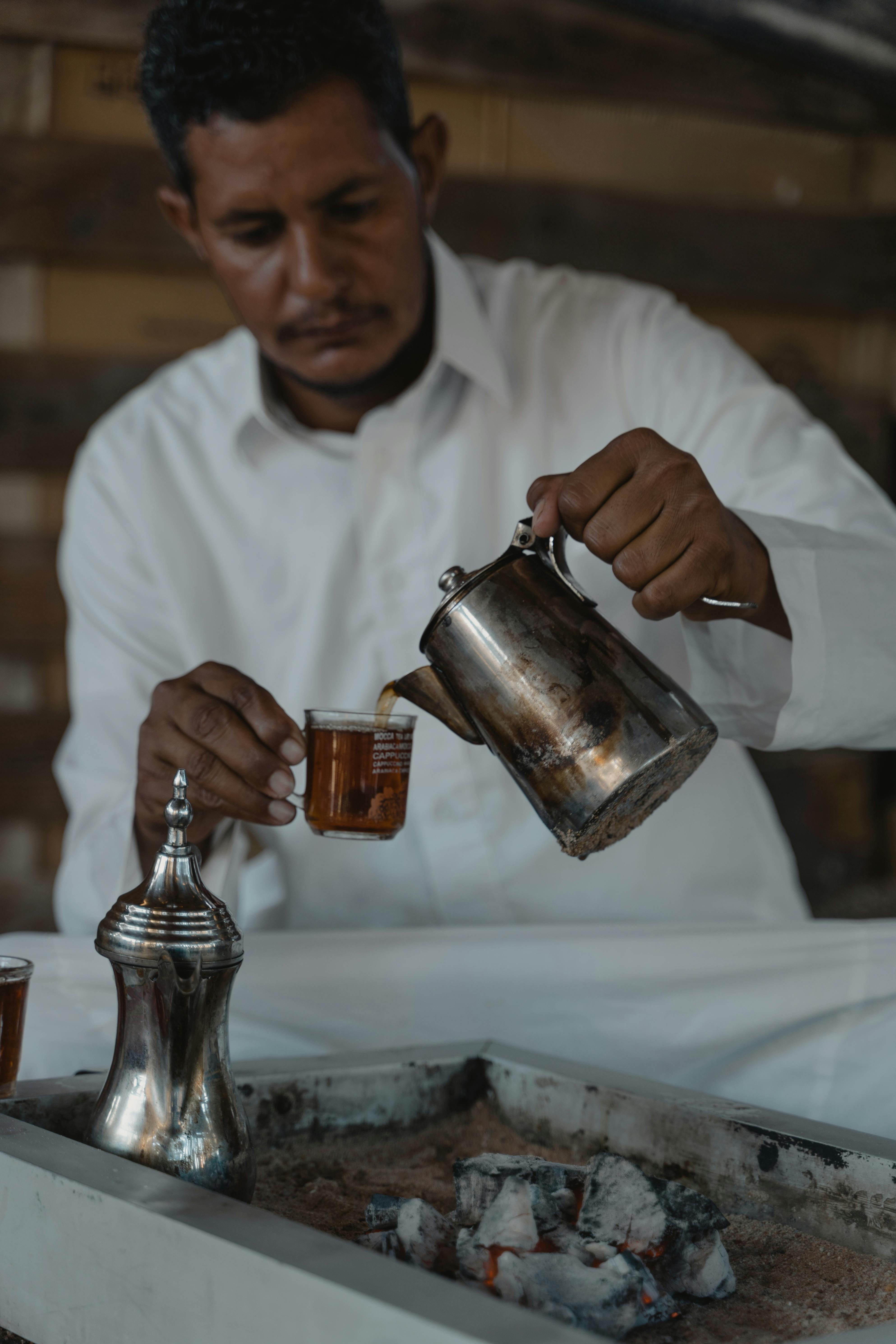 A Man in a White Long Sleeved Shirt Pouring Tea from a Stainless Kettle ...