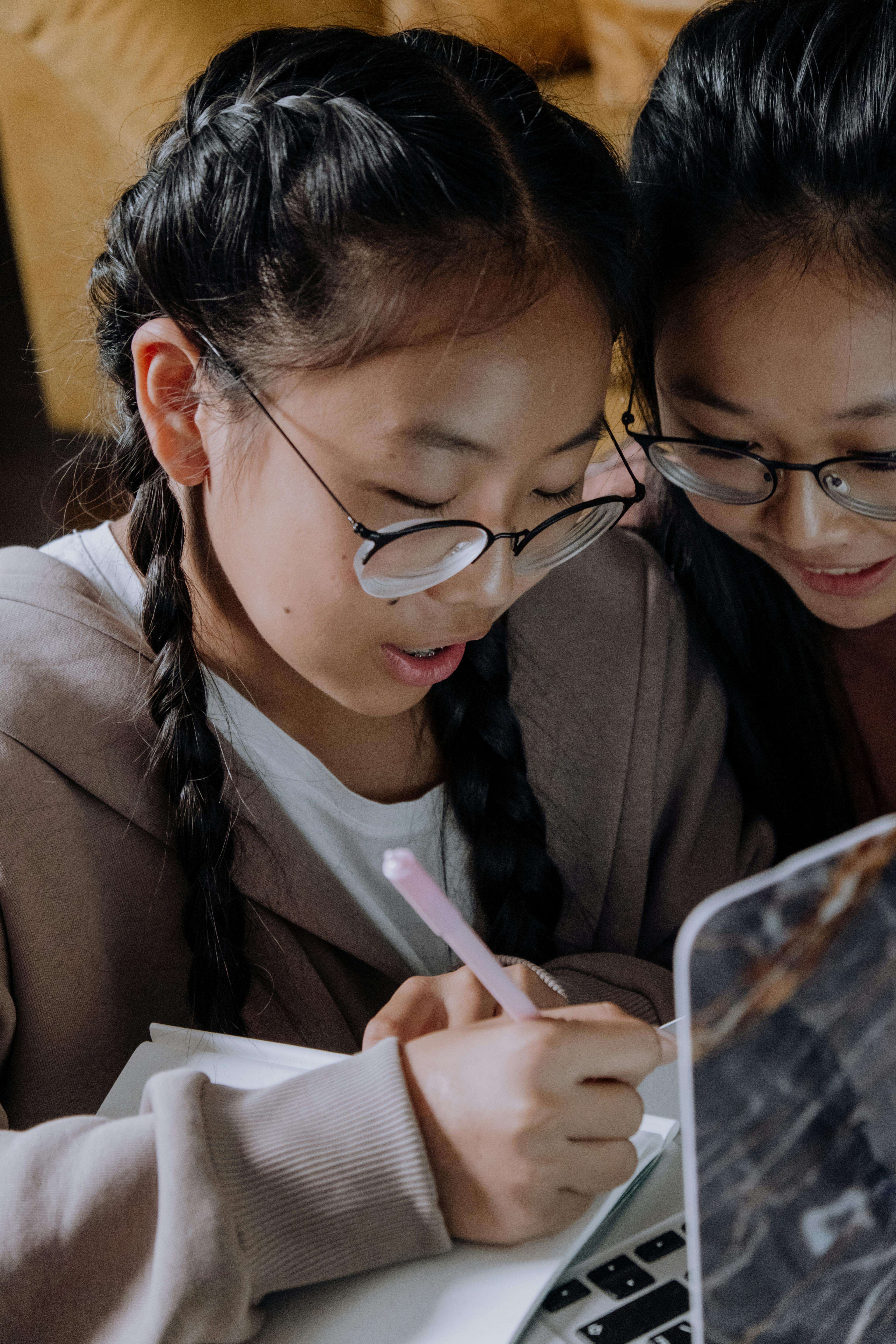 A Two Girls Wearing Eyeglasses While Writing · Free Stock Photo