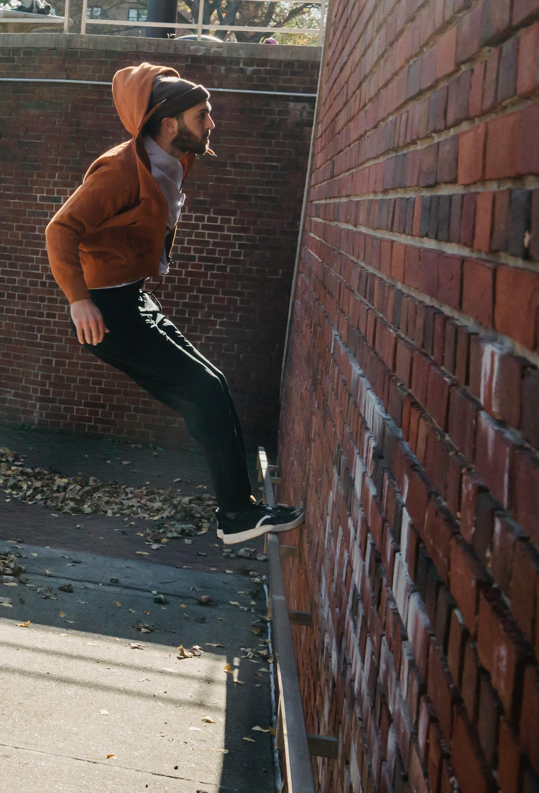 Focused man balancing on metal ledge on brick wall · Free Stock Photo