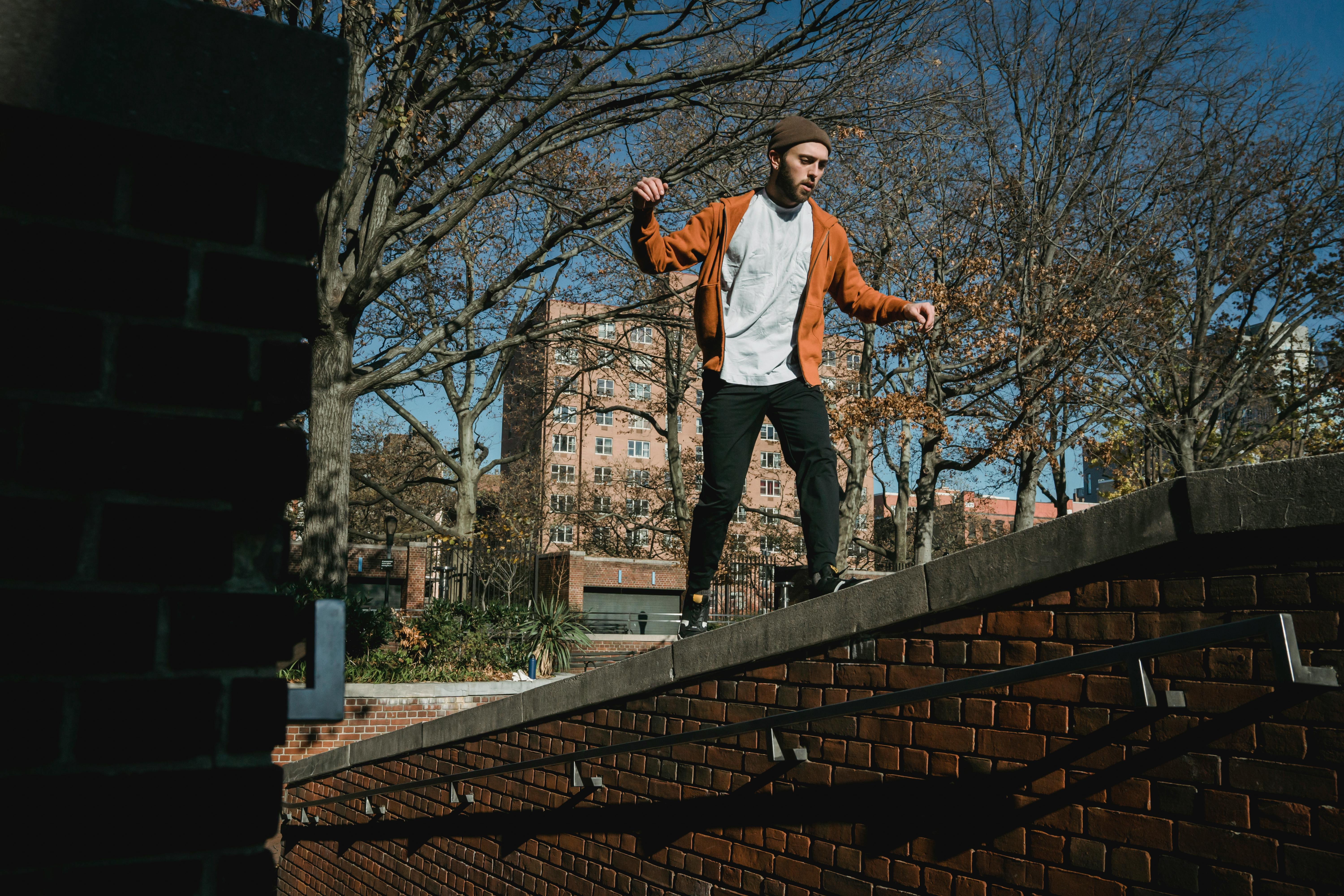Focused man walking on brick parapet in city park · Free Stock Photo