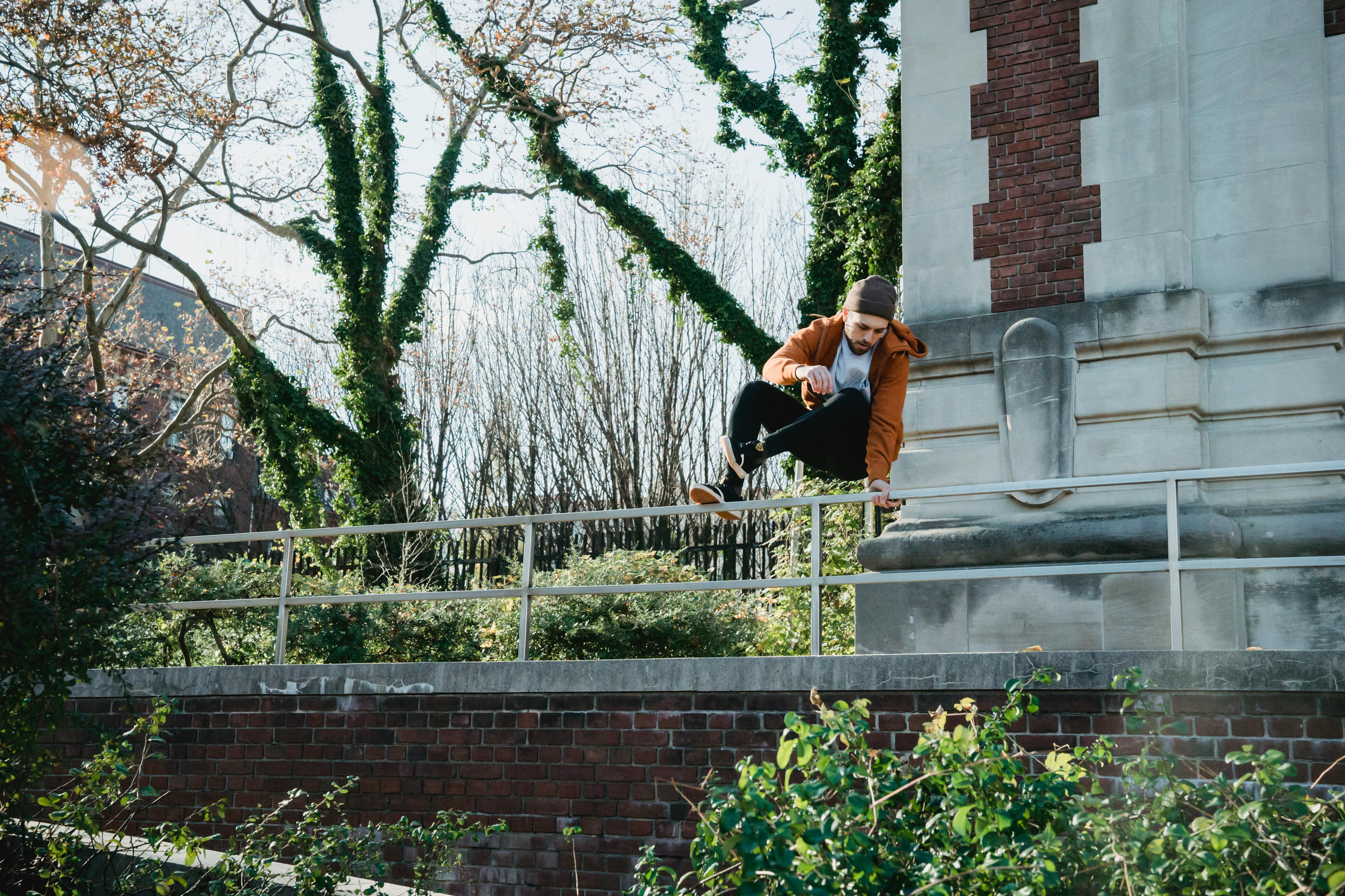 Sporty man jumping over railing near brick building · Free Stock Photo