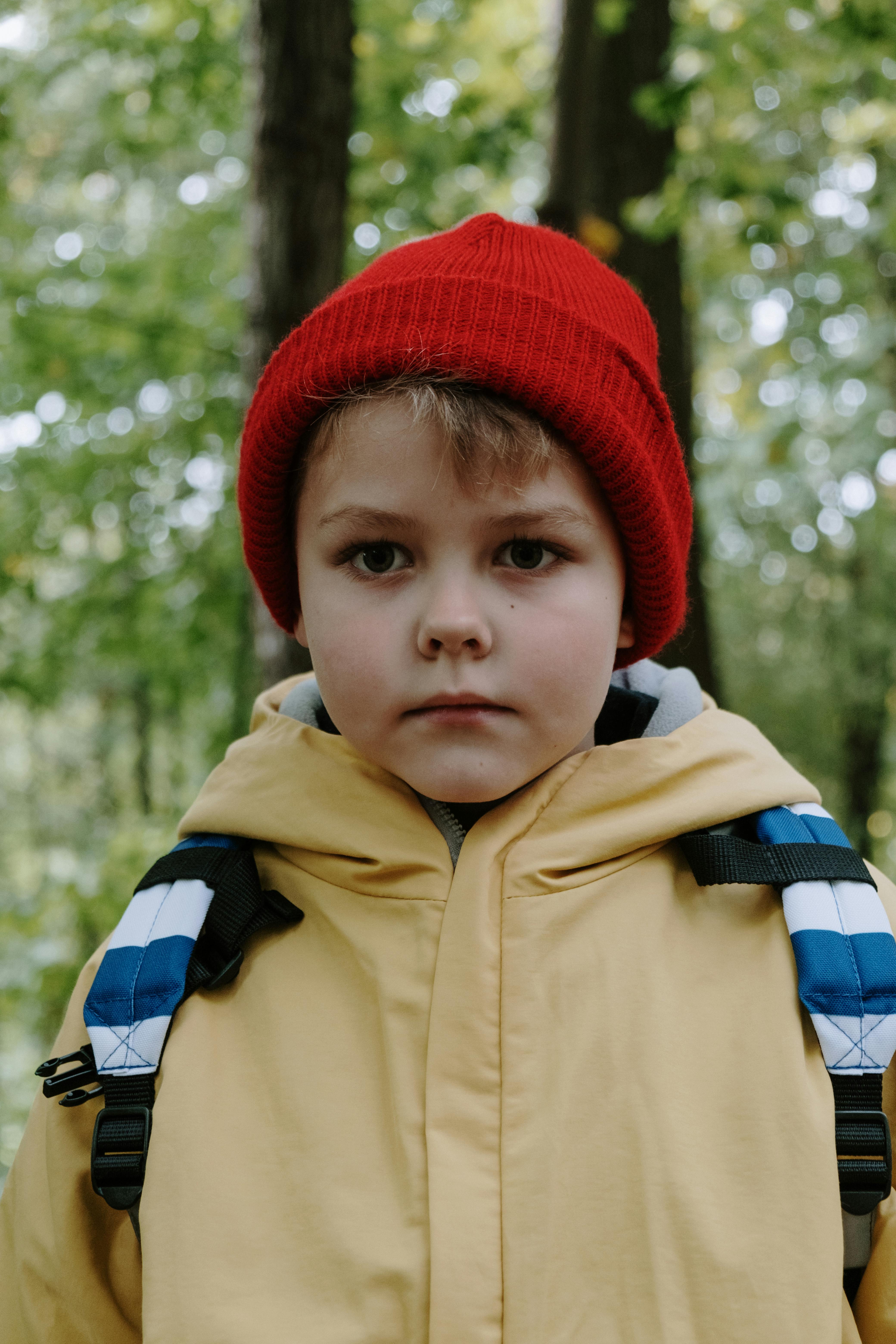 A Boy in Yellow Jacket Near Tree Trunks · Free Stock Photo