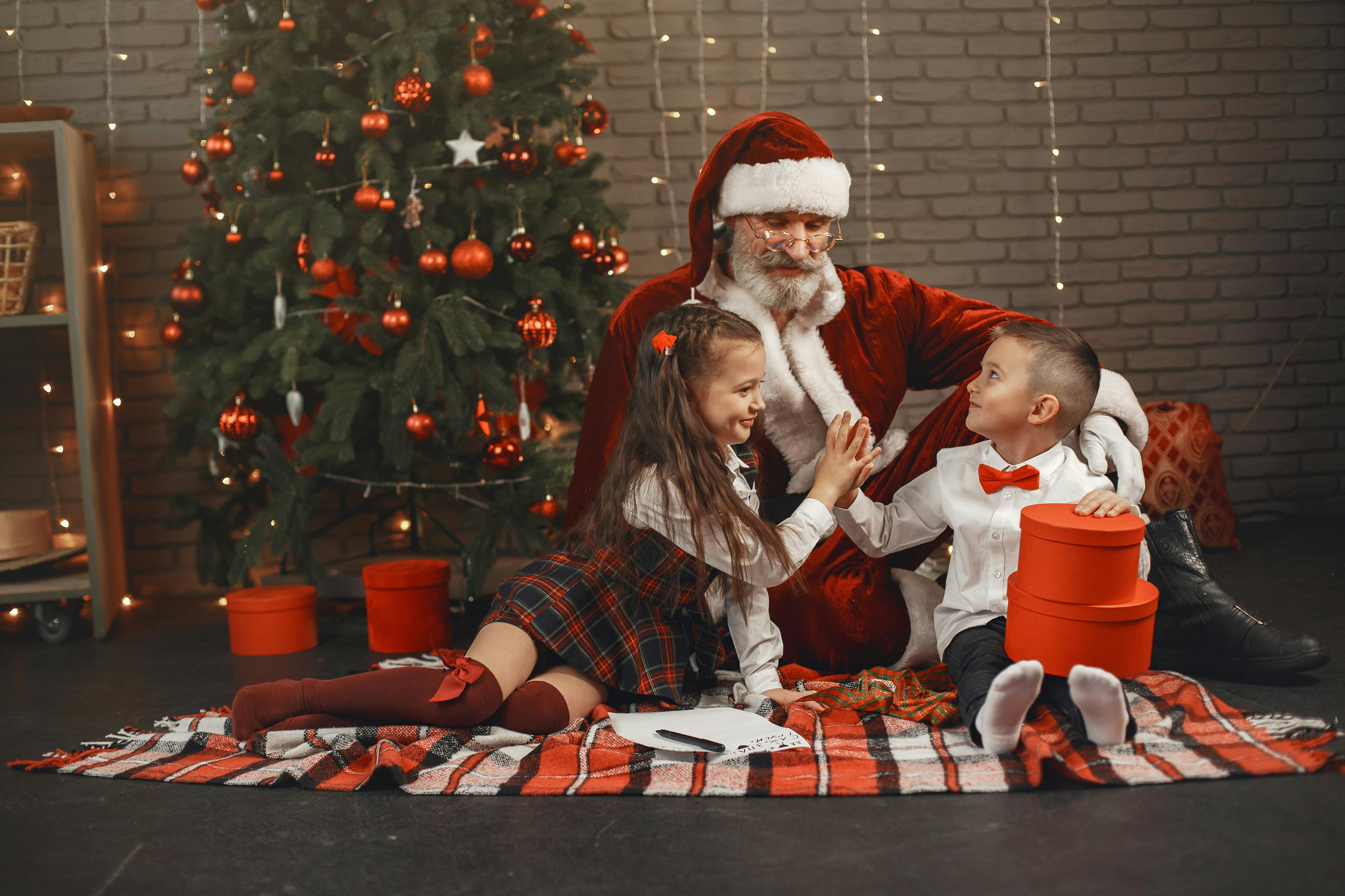 Man in Santa Costume Sitting with a Boy and a Girl Beside a Christmas ...