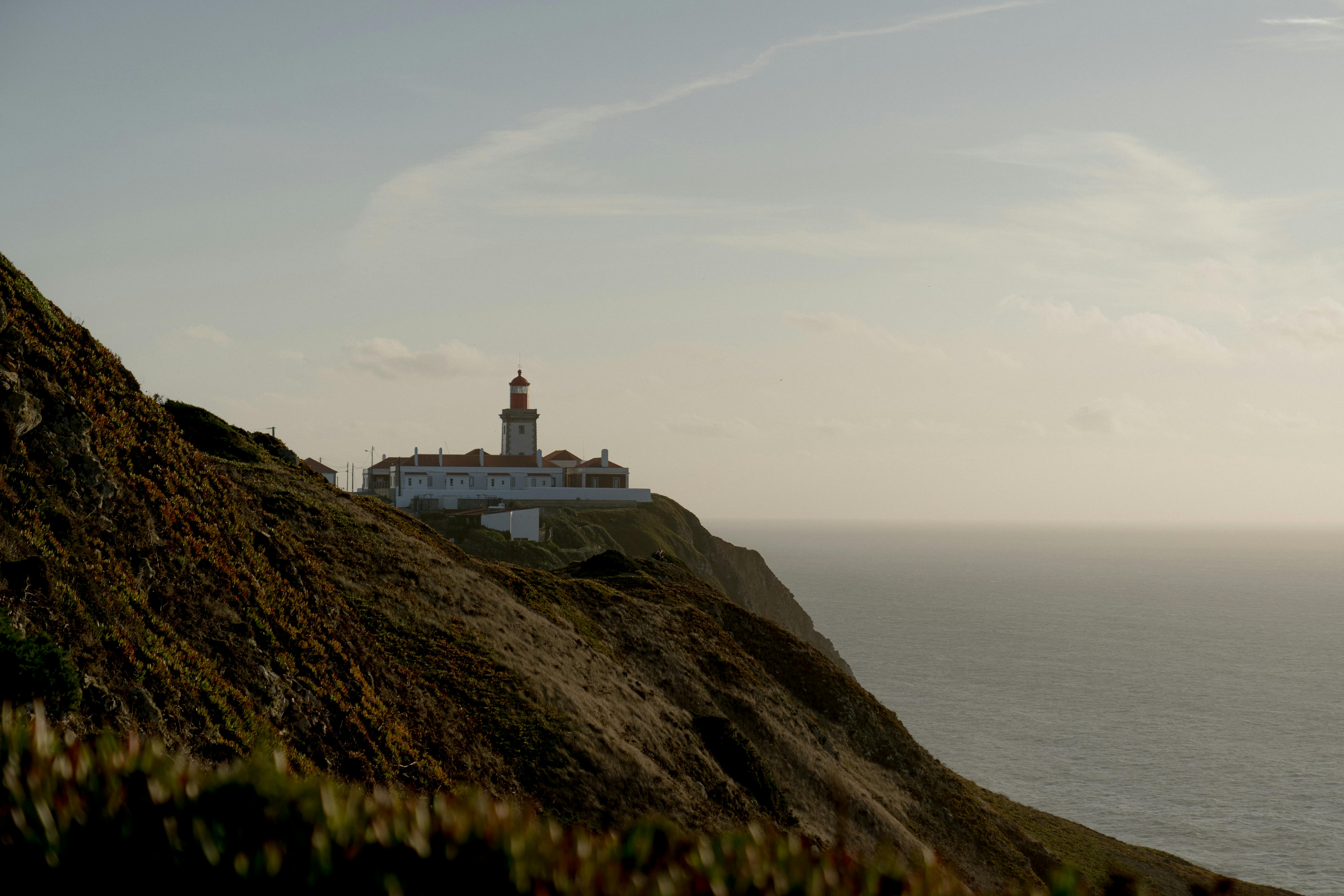 A Lighthouse on Mountain Cliff Near Body of Water · Free Stock Photo