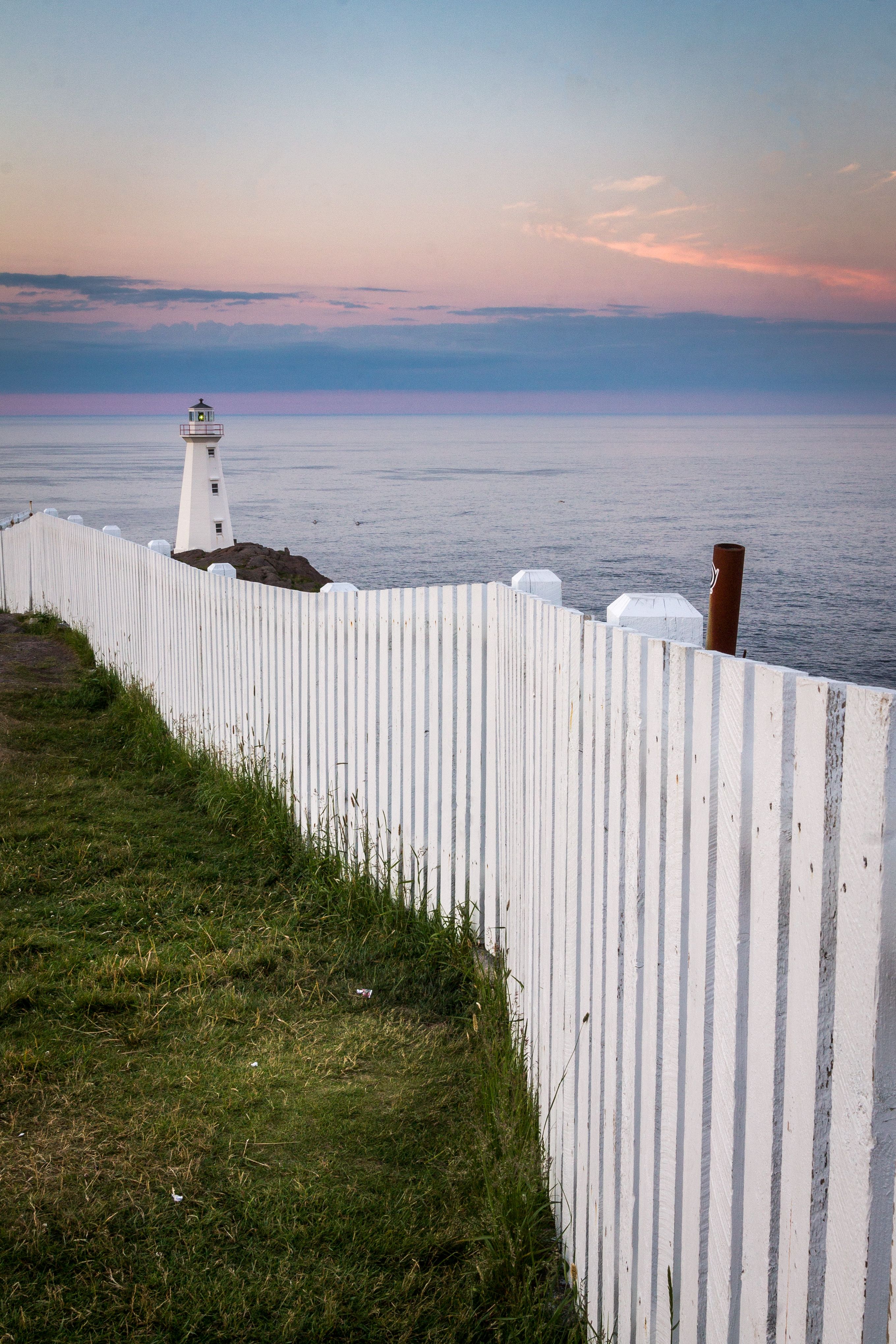 Lighthouse placed on seacoast behind fence · Free Stock Photo