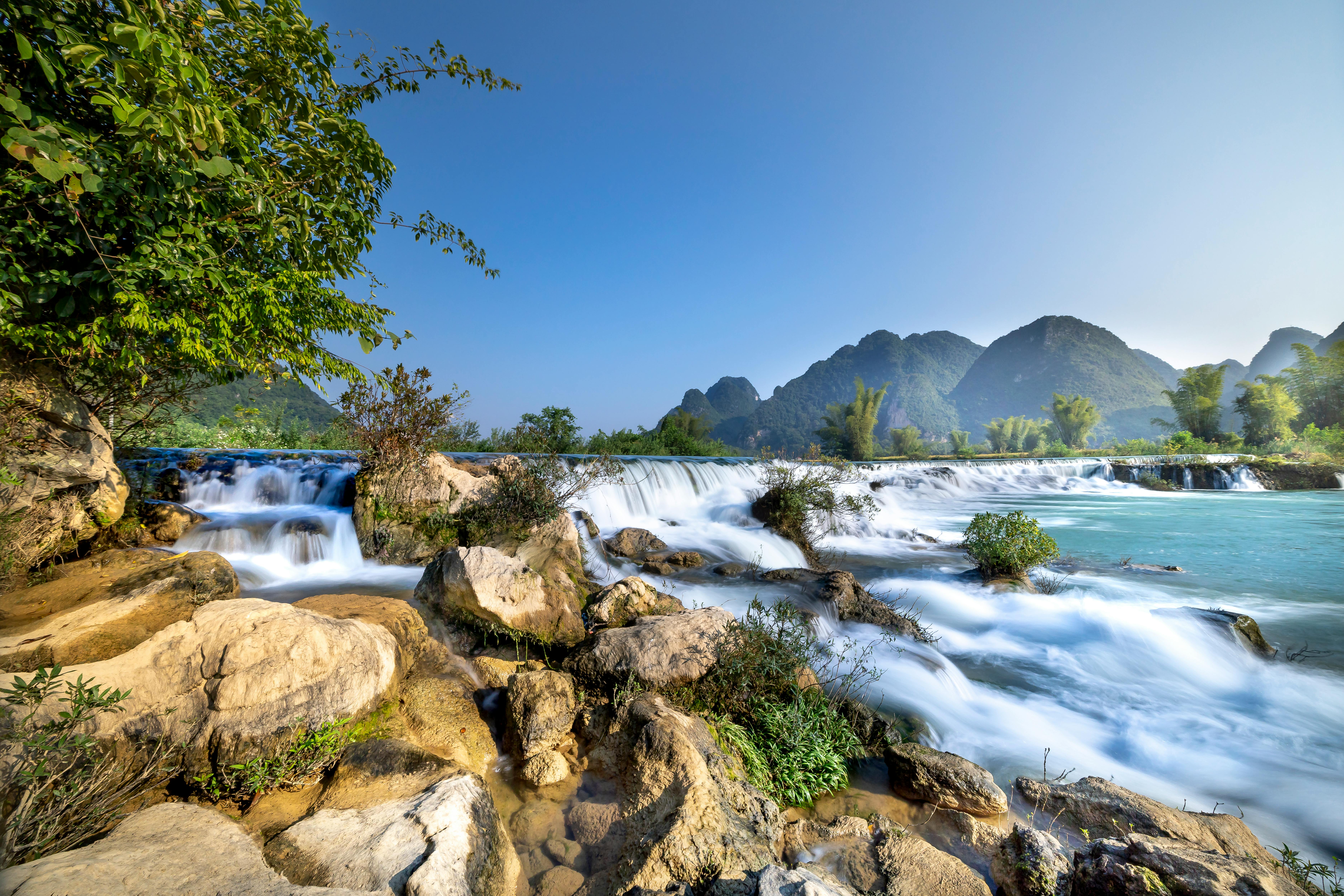 Breathtaking landscape of waterfall near rocky coast and green hills ...