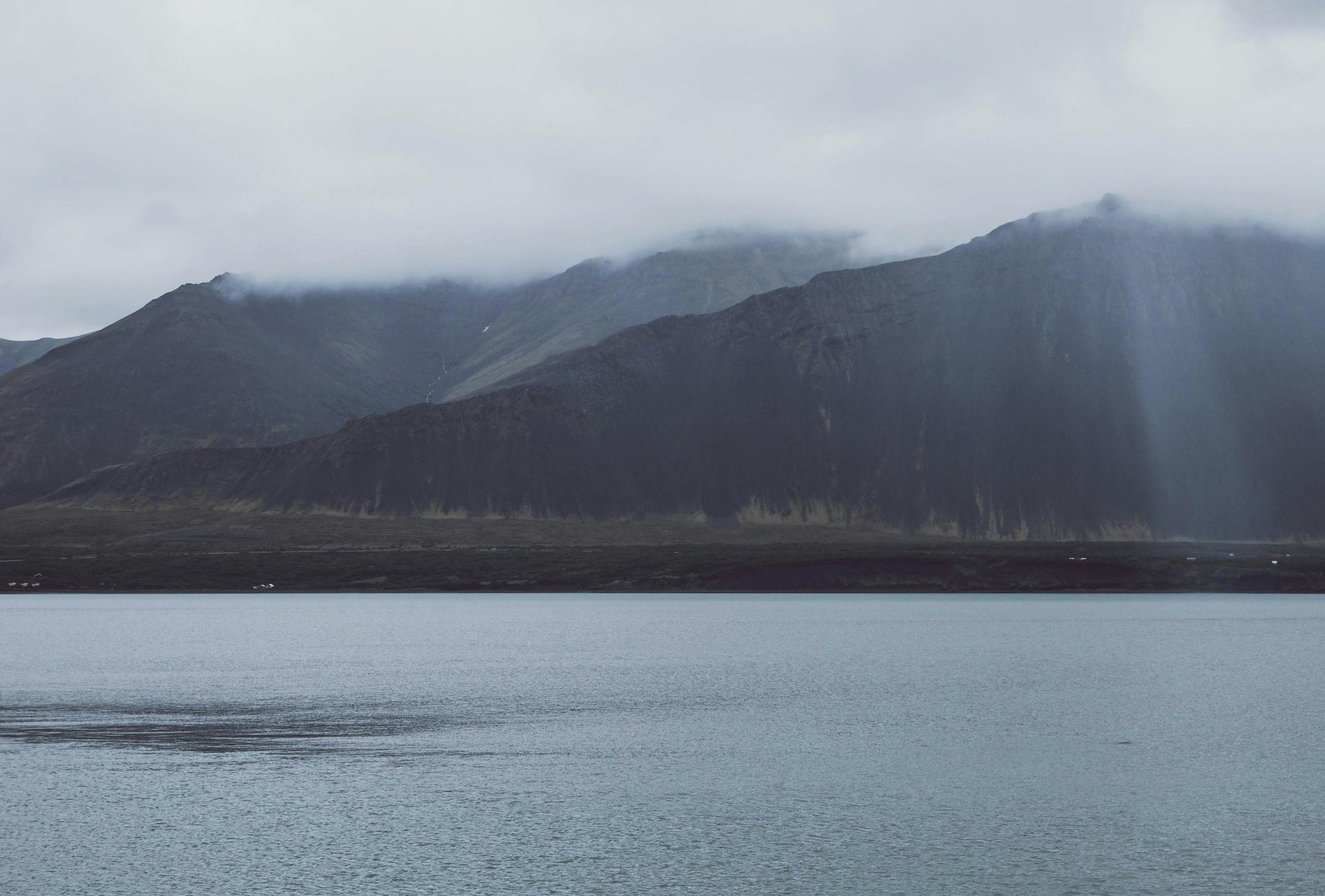 Rippling lake amidst rocky mountains against cloudy sky · Free Stock Photo