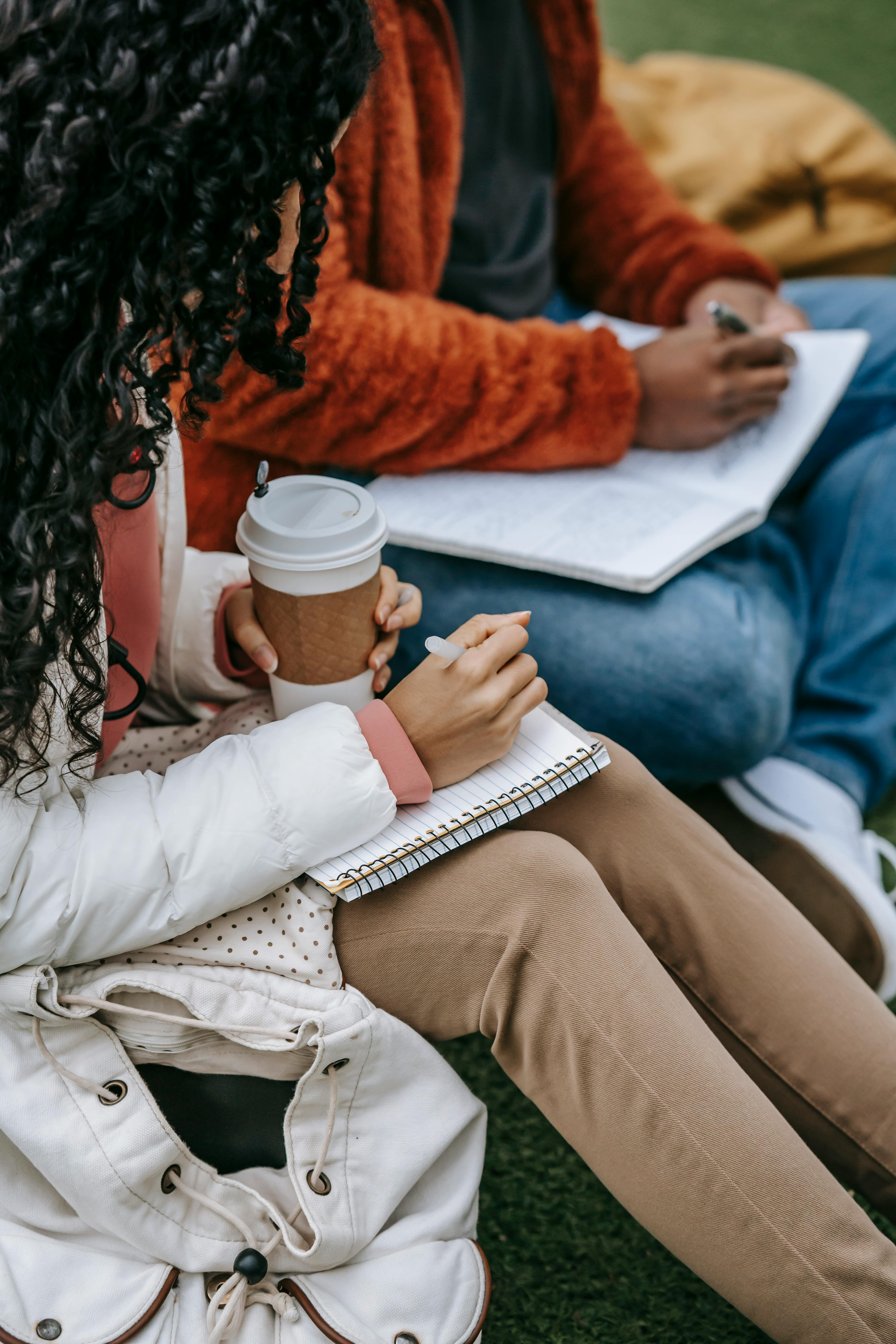 Crop multiracial students writing in notebooks on street · Free Stock Photo
