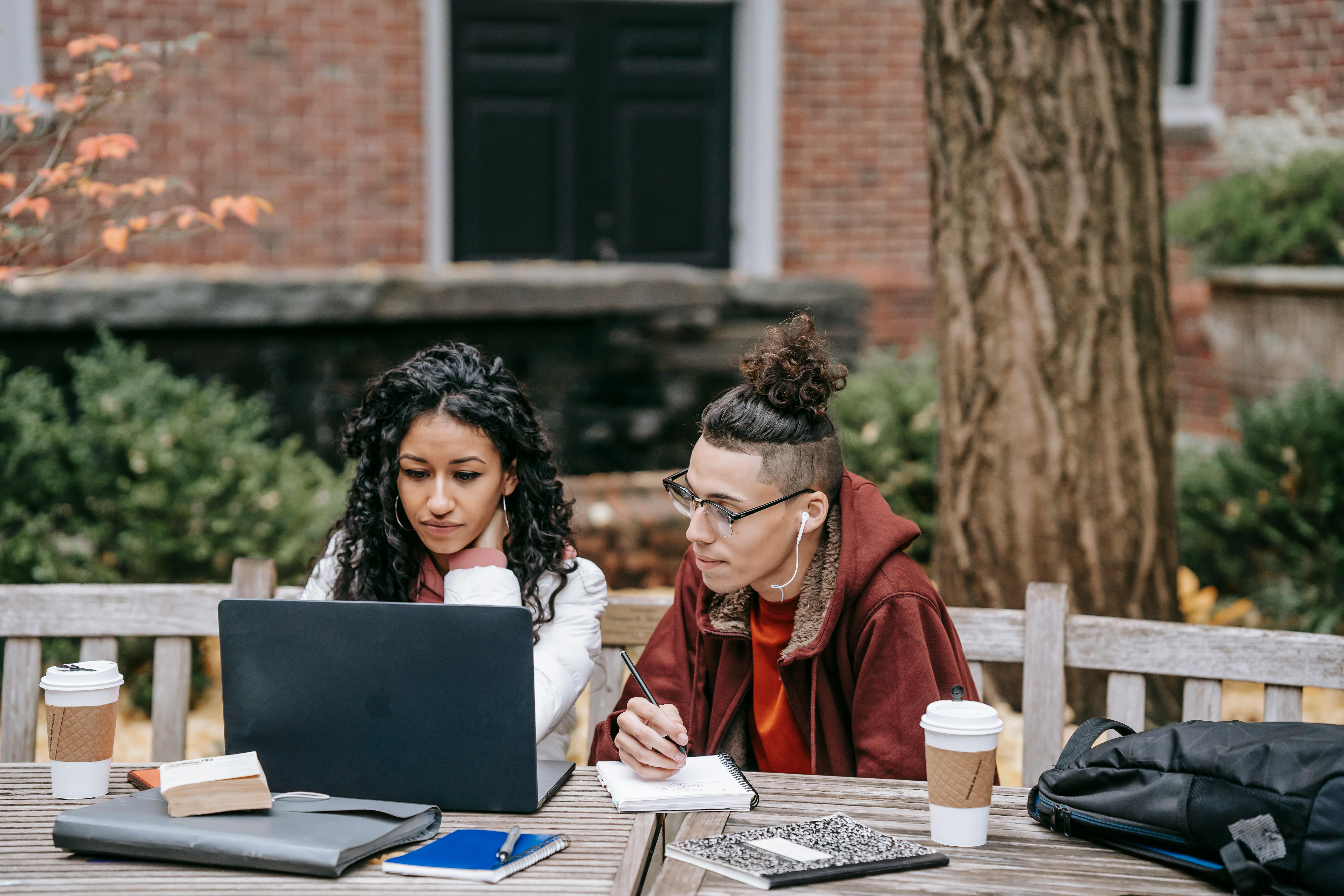 Diverse focused students working with laptop at table in yard · Free ...
