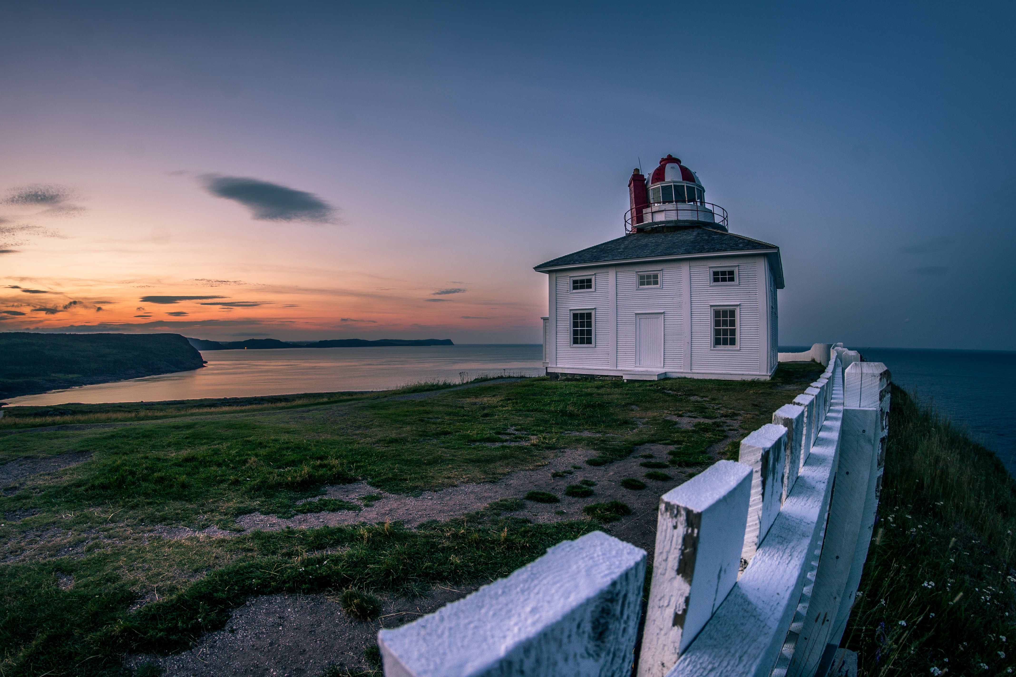 Lighthouse on shore with fence against sea at sunset · Free Stock Photo