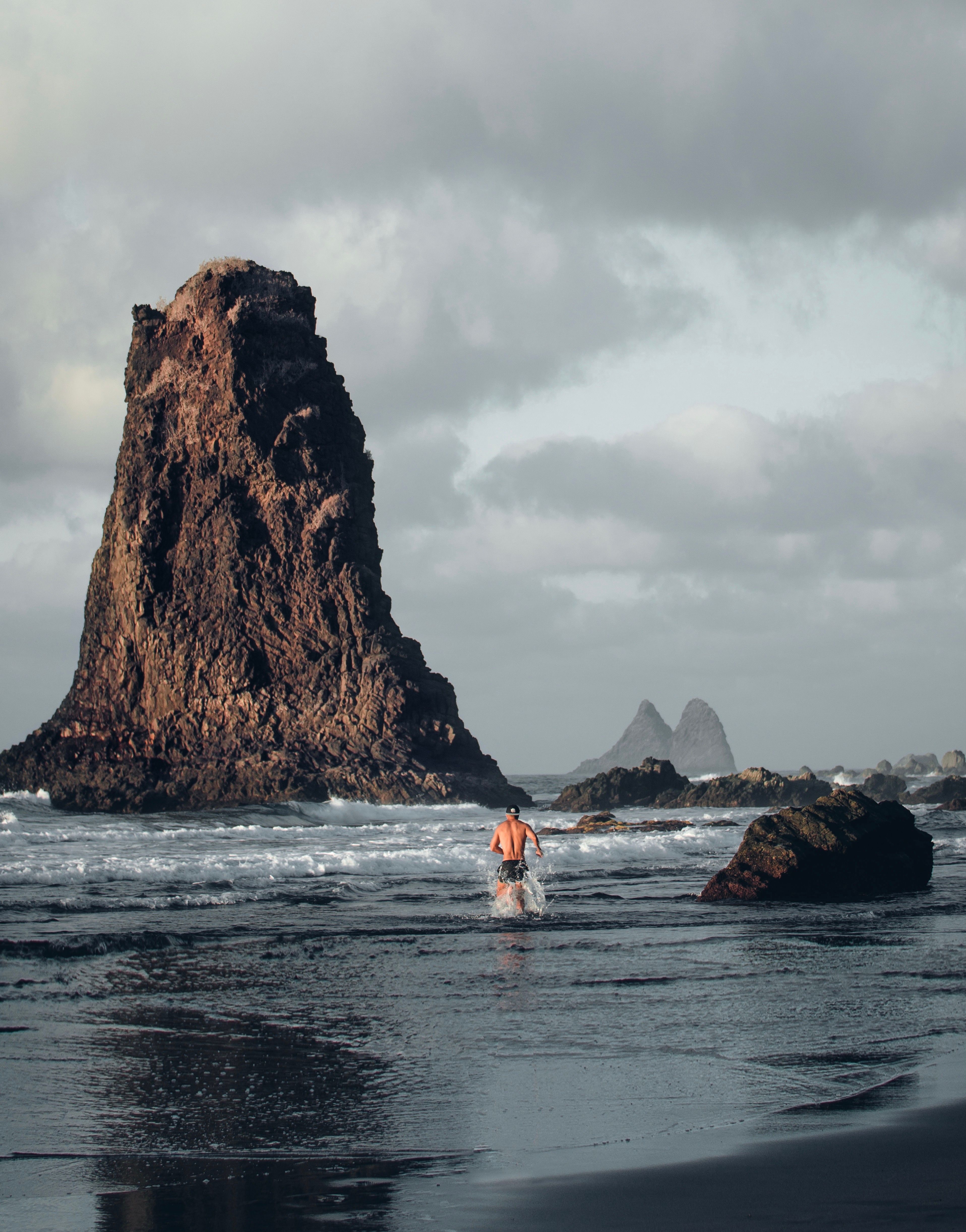 Man running in water of ocean with rocky cliffs · Free Stock Photo
