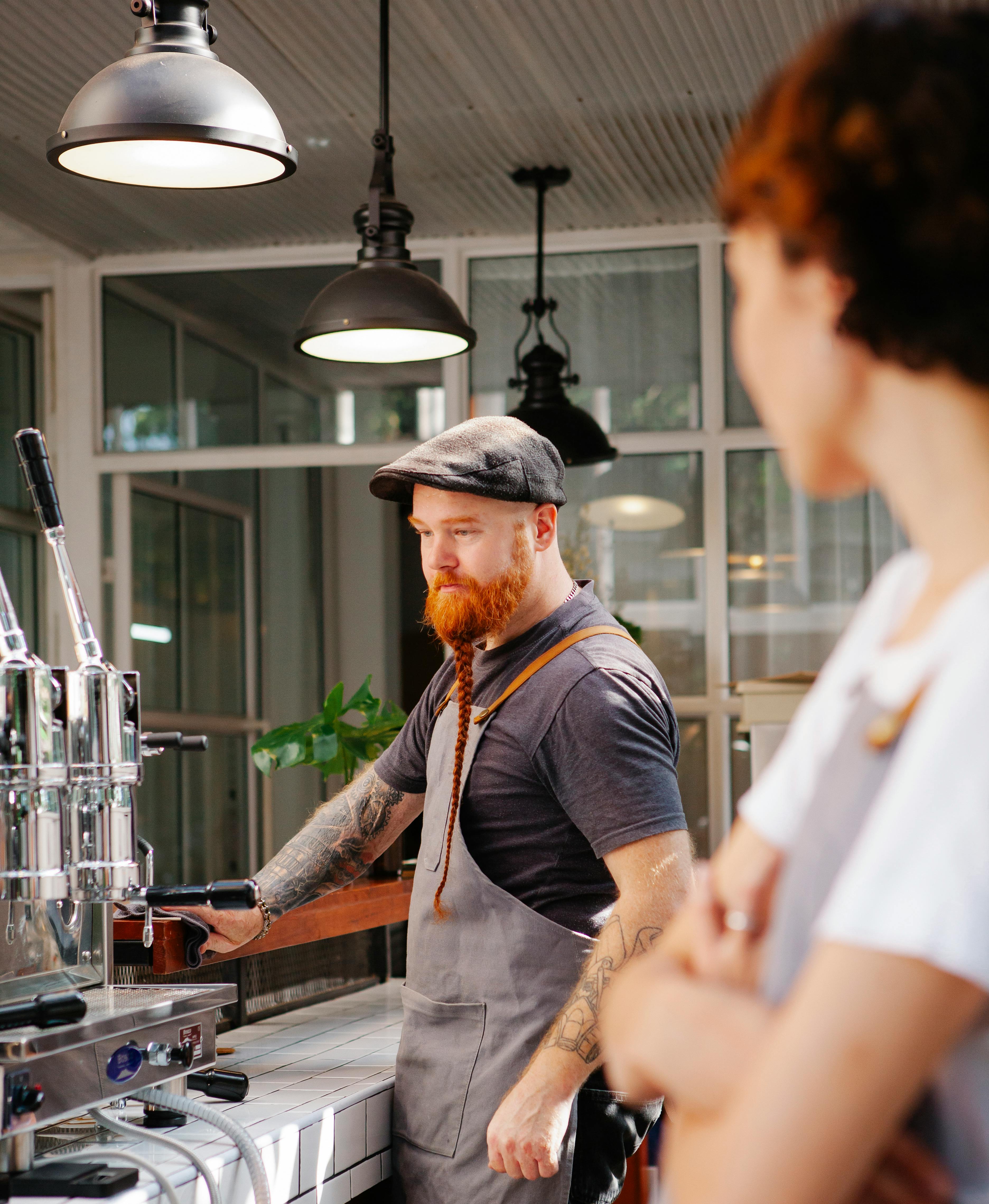 Cheerful hipster barista talking to colleague with coffee at counter ...