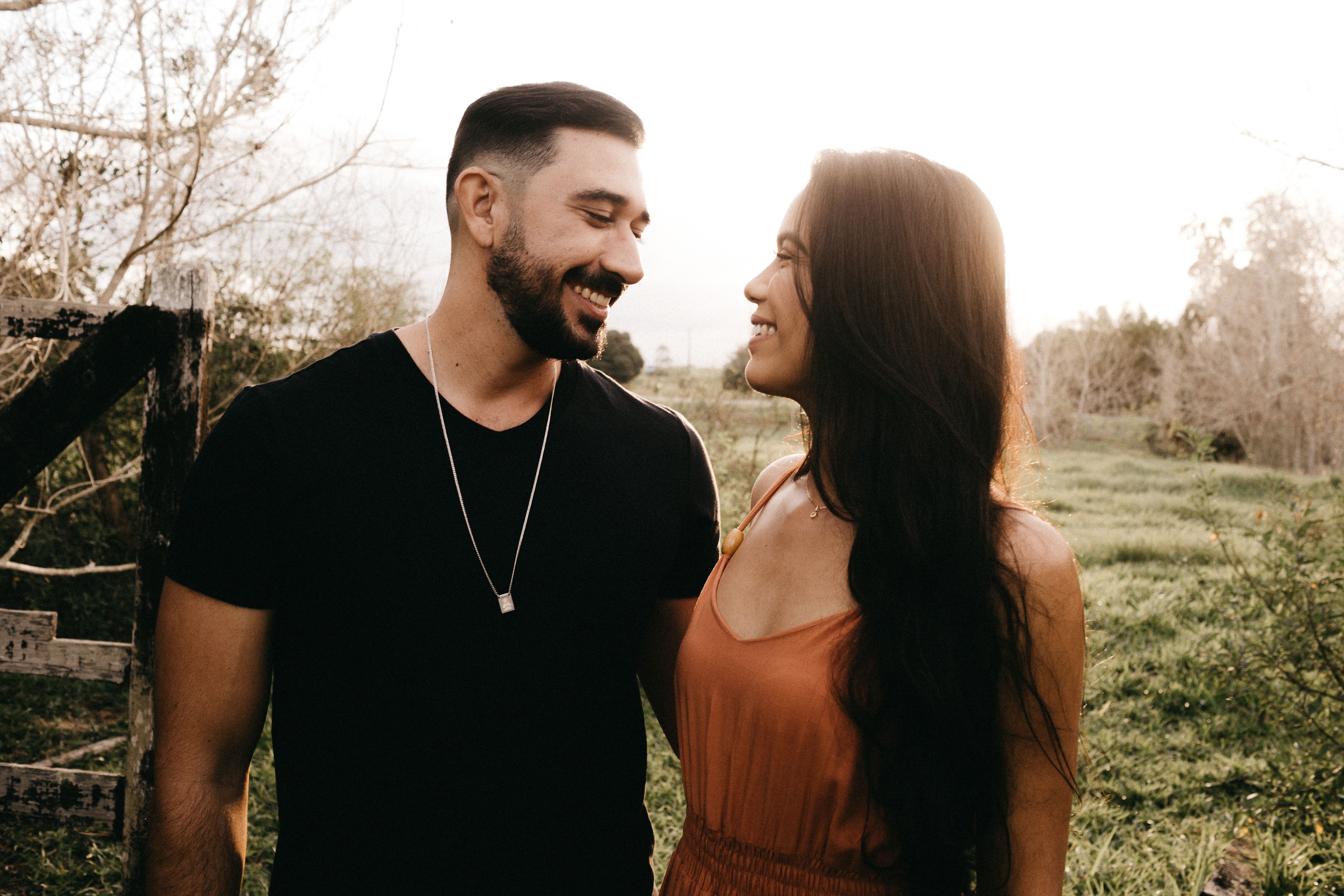 Smiling Hispanic couple embracing on meadow in sunshine · Free Stock Photo