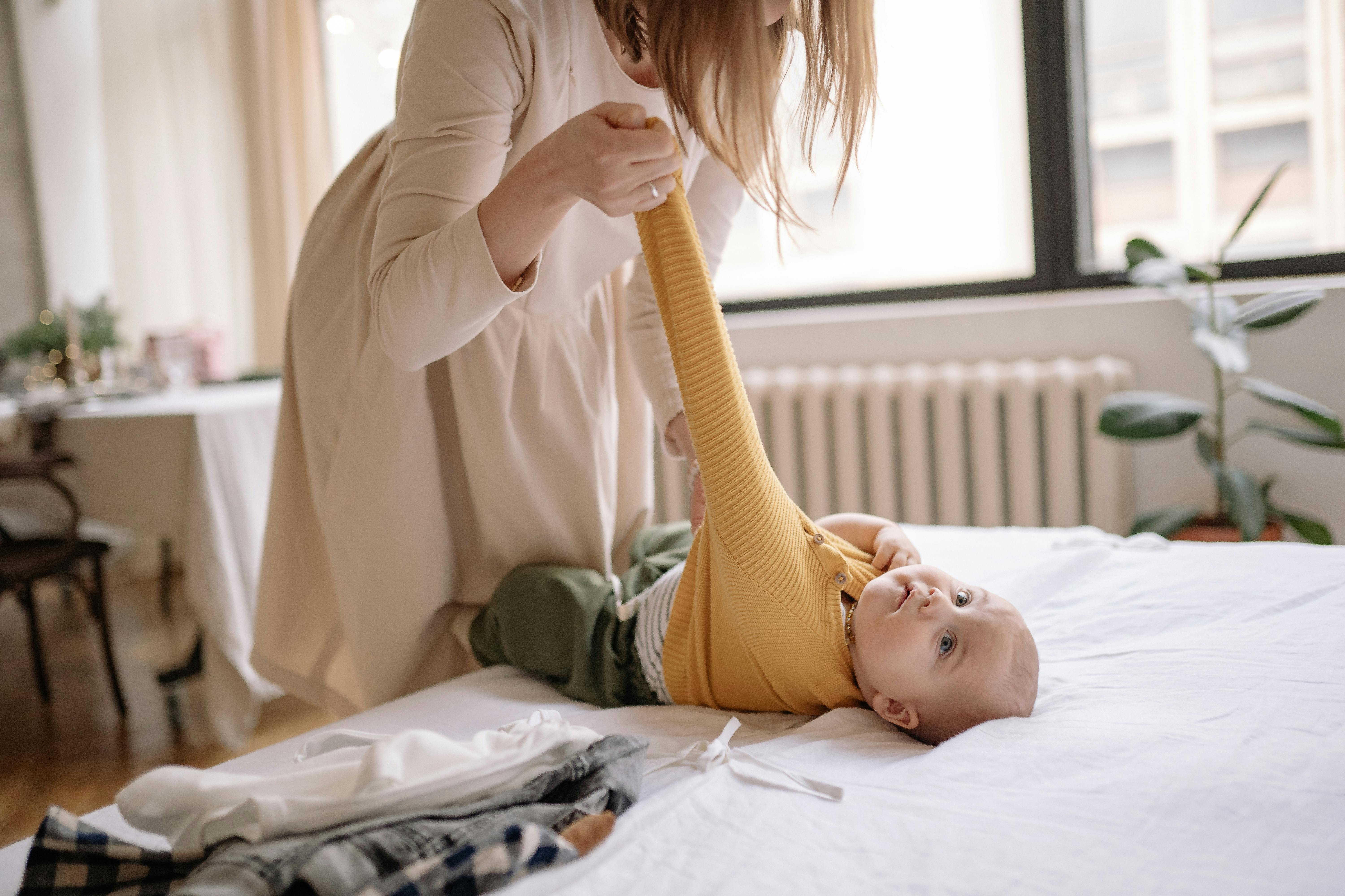 A Mother Taking Off Her Baby's Yellow Sweater · Free Stock Photo