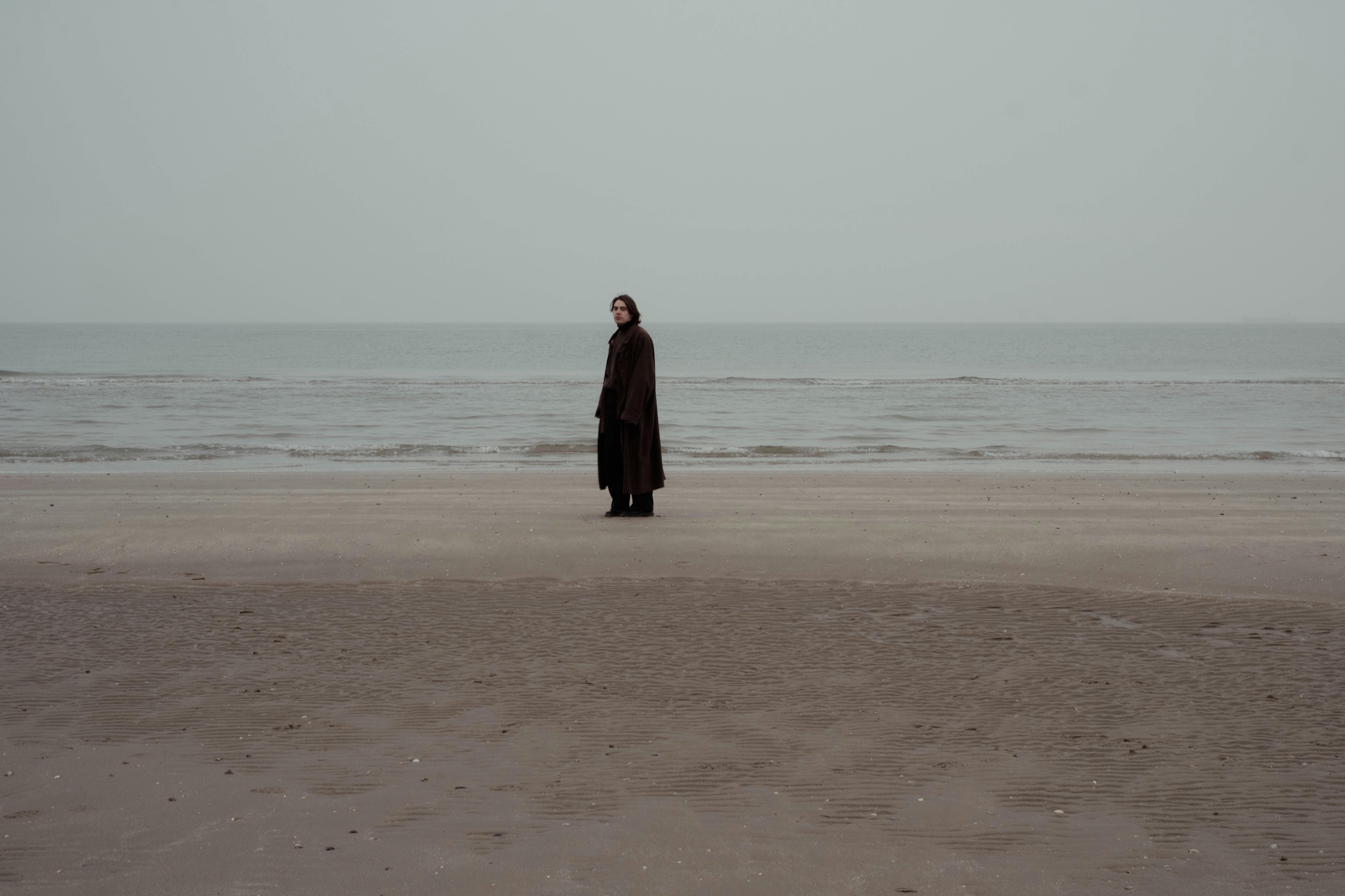 Stylish man model standing on sandy coast near sea · Free Stock Photo