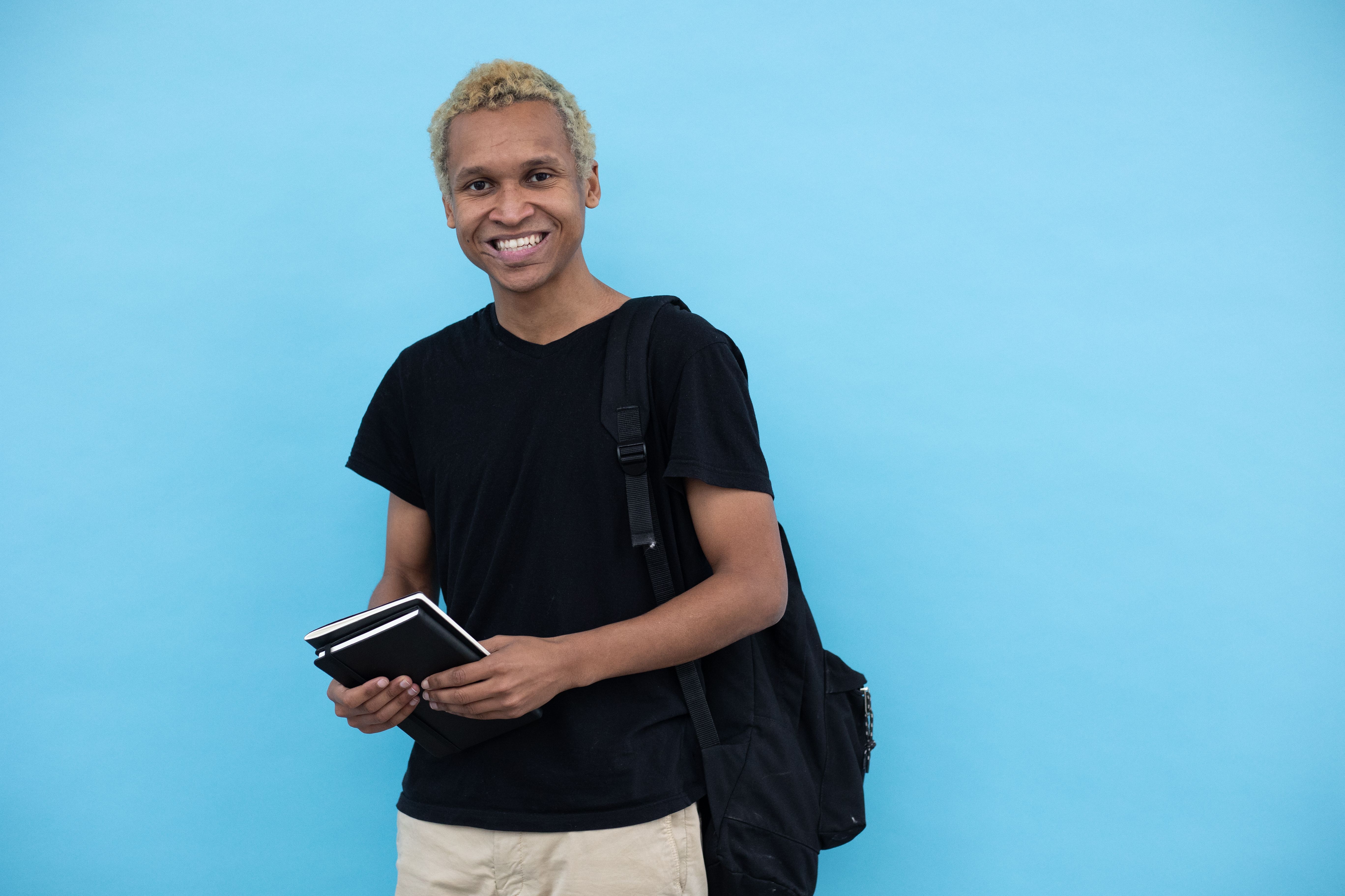 Happy black student with backpack and notebooks against bright ...