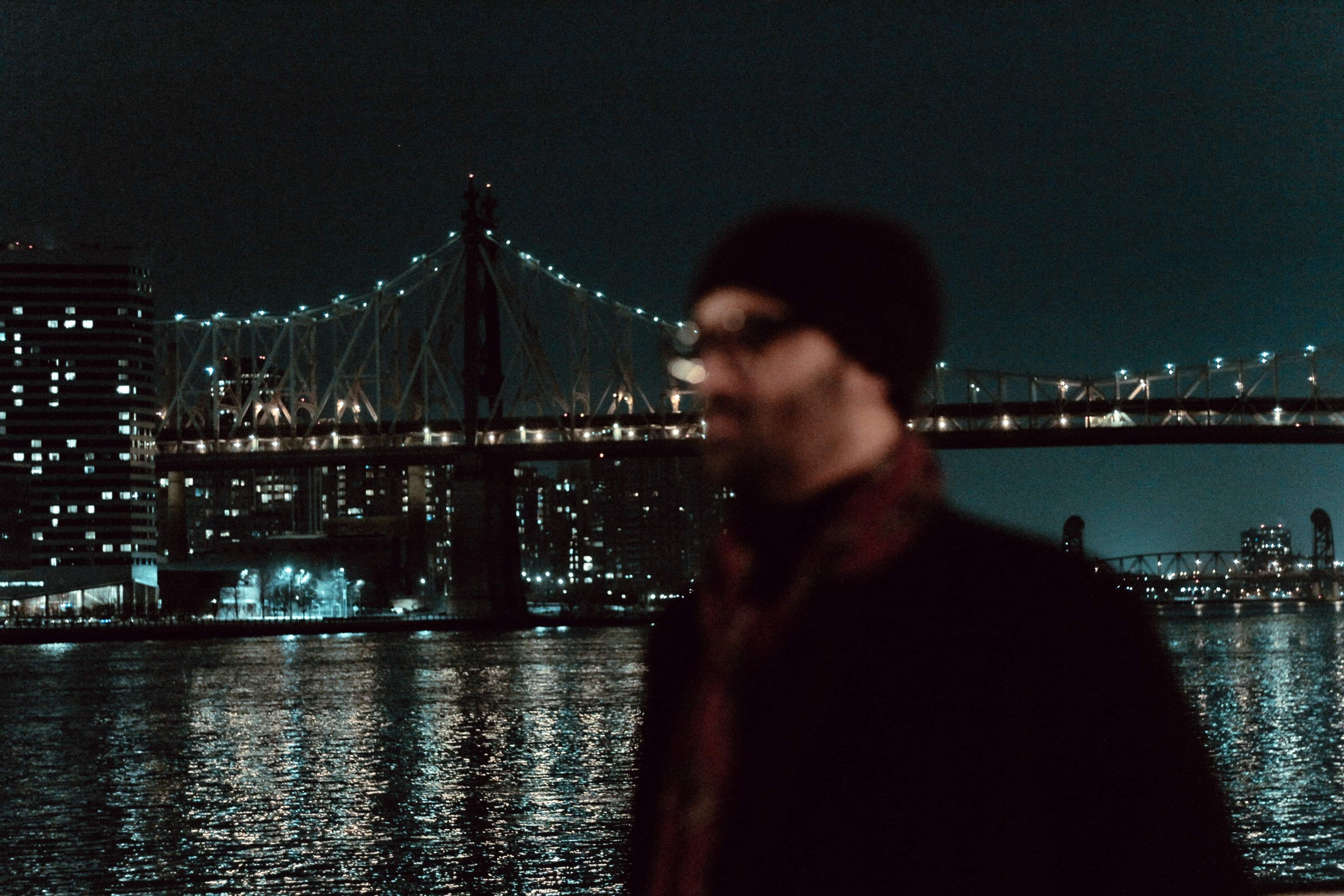 Man near river and glowing bridge near buildings in city · Free Stock Photo